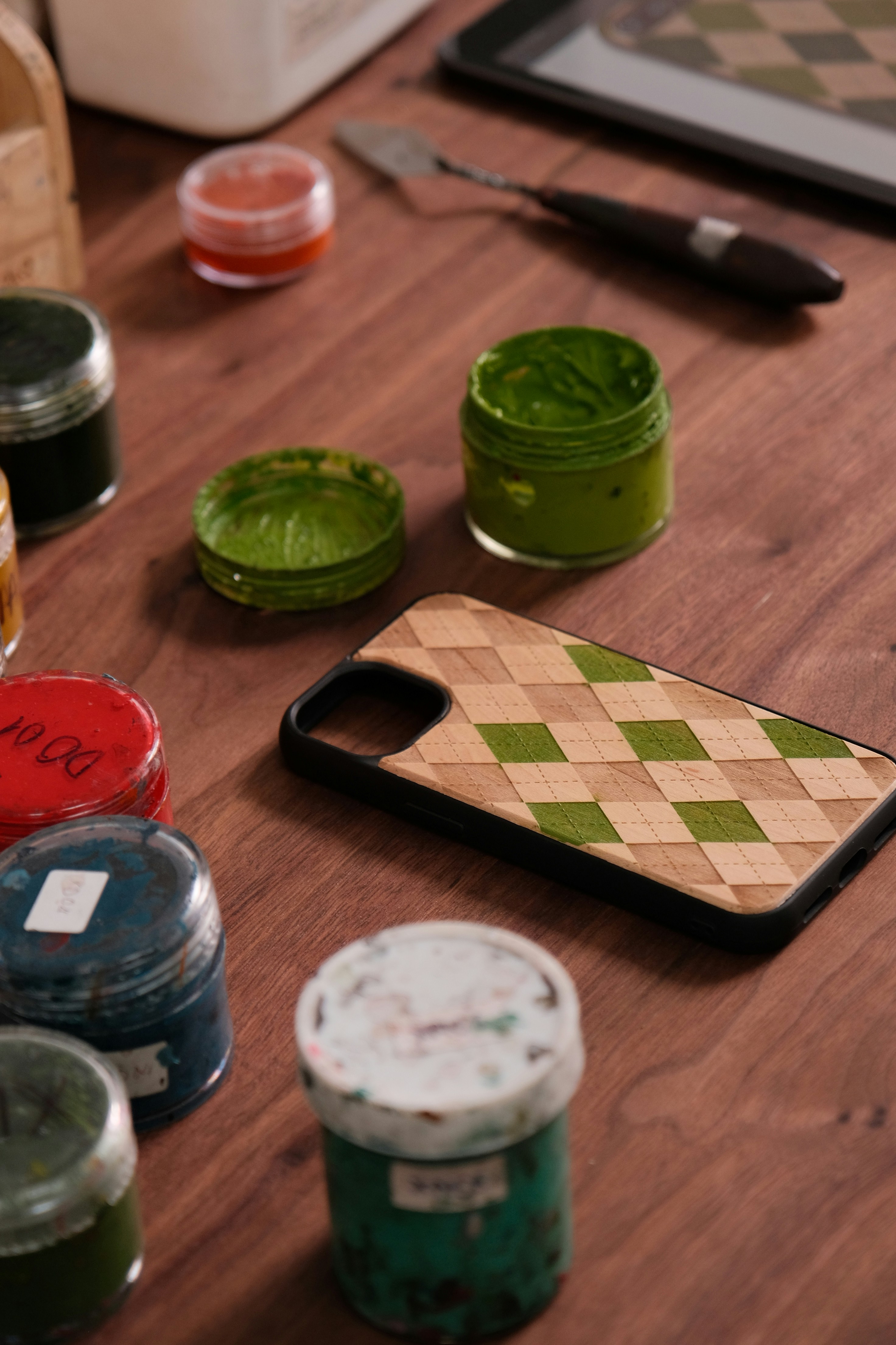 Palette of Greens: Paint Pots and a Geometric Phone Case on a Wooden Surface