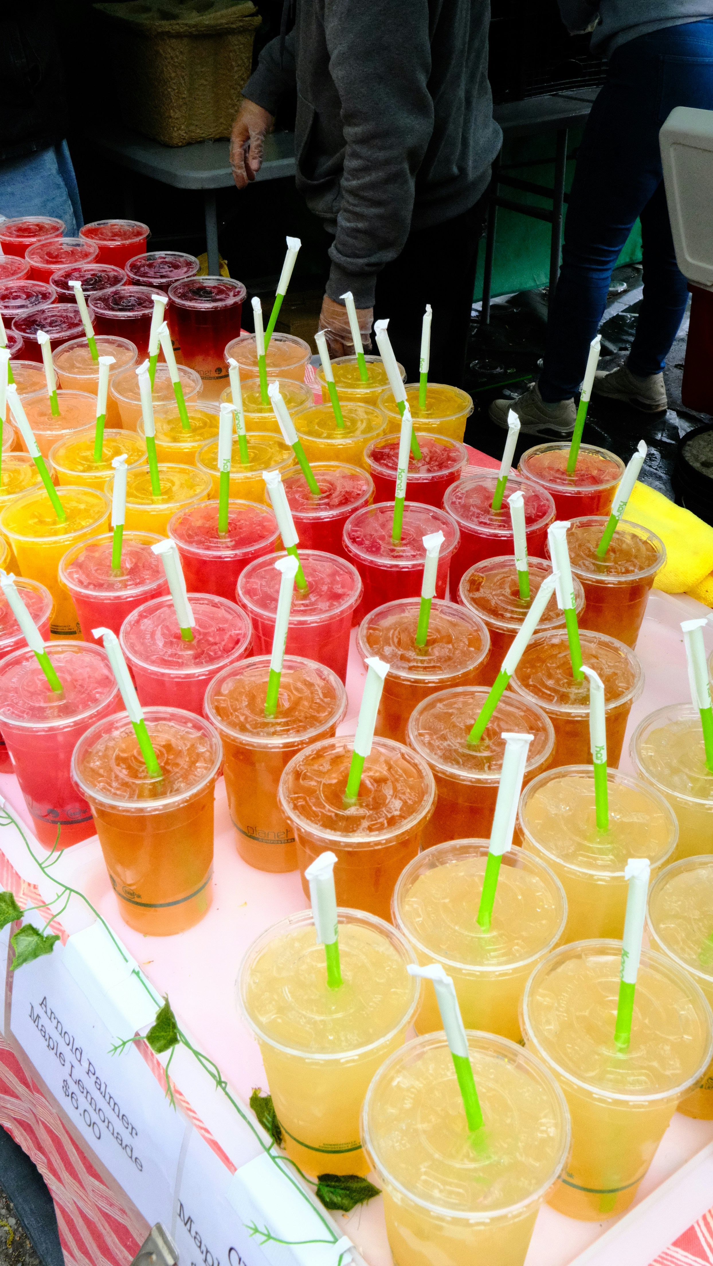 Many colorful iced drinks with straws on a market stall.