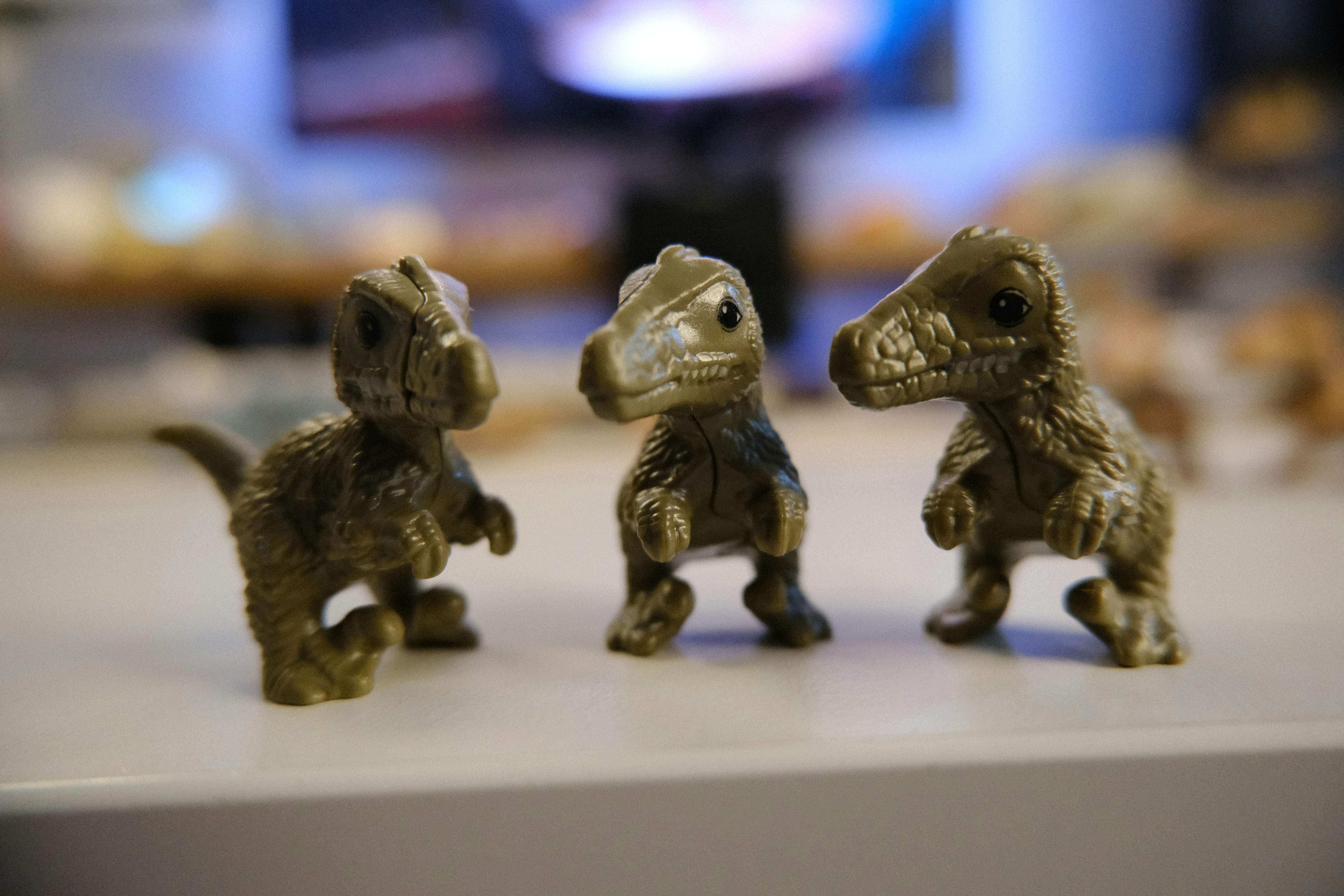 Three small green dinosaur toys standing on a white surface.