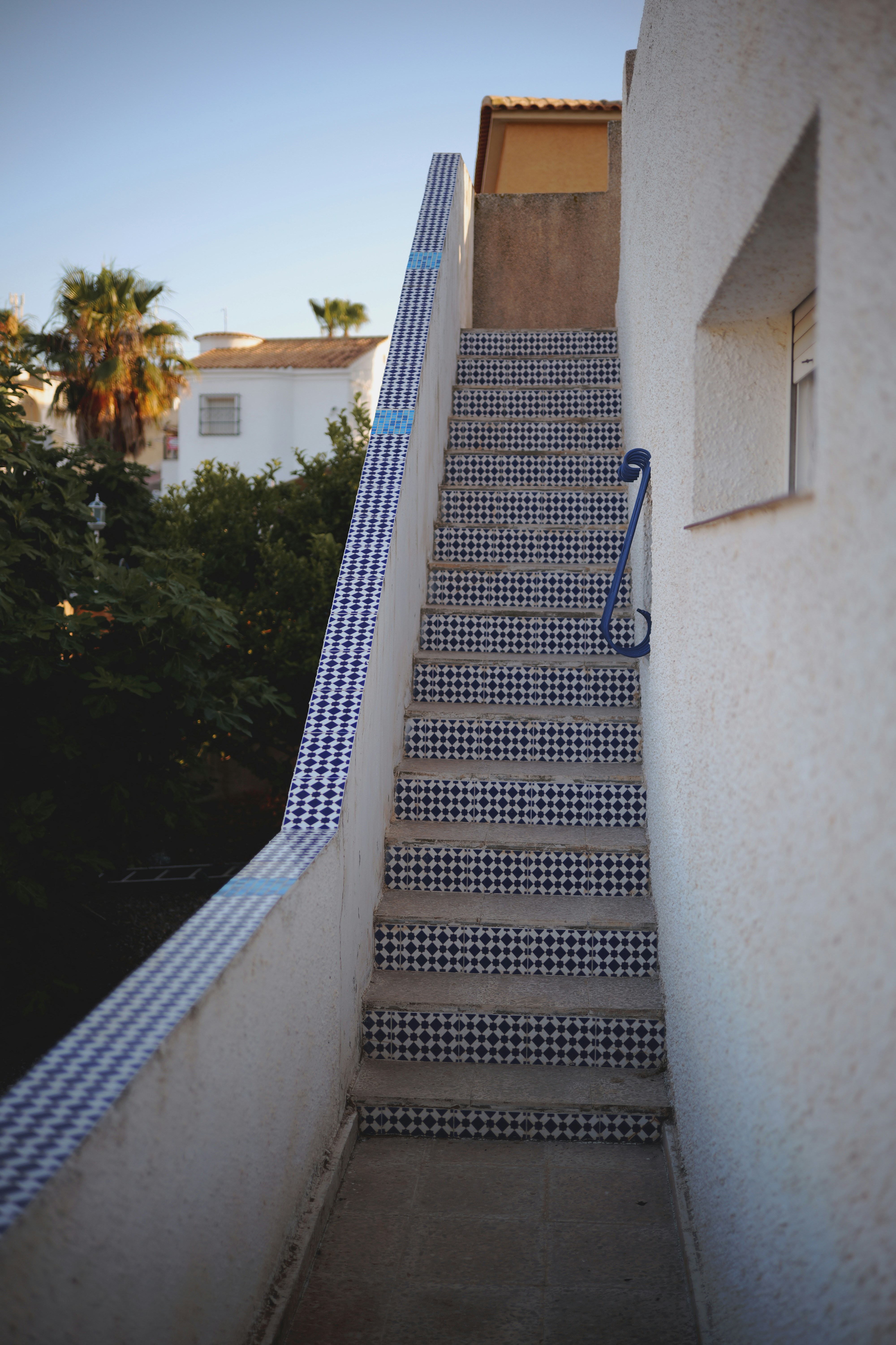 Blue-Tiled Staircase Ascending Along Sunlit White Wall