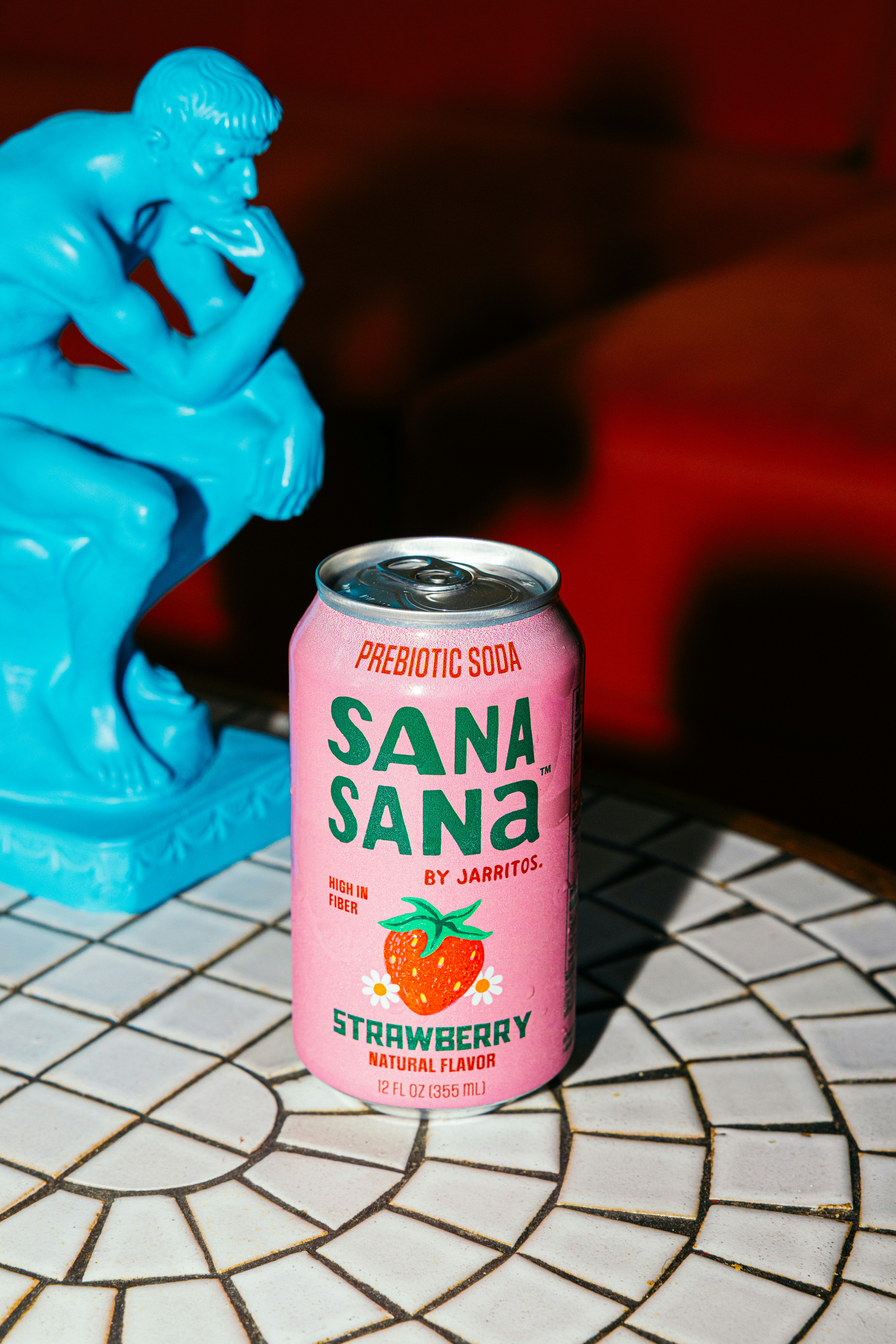 Blue statue watches a pink strawberry soda can