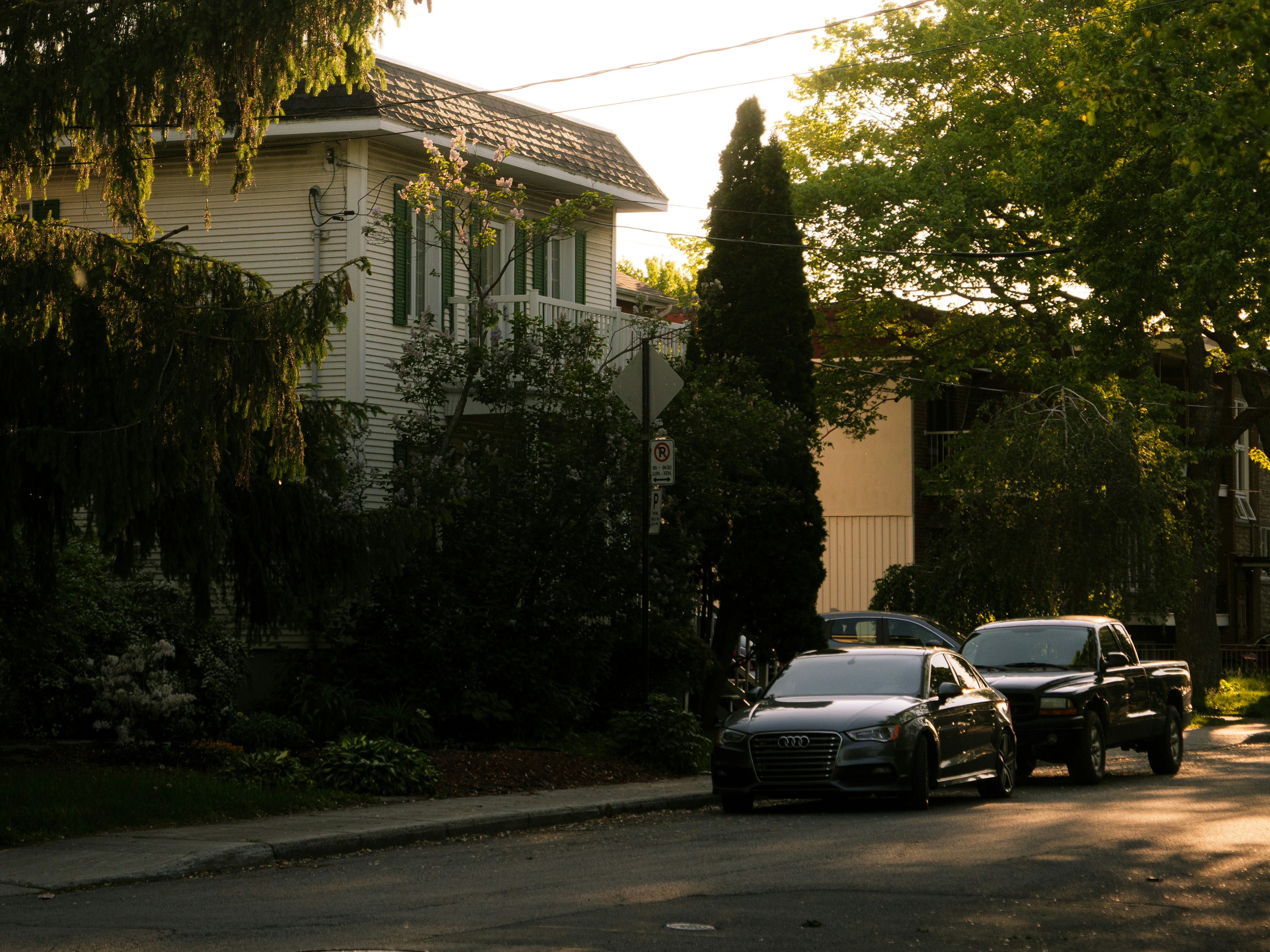 Cars parked on a street with a house and trees.
