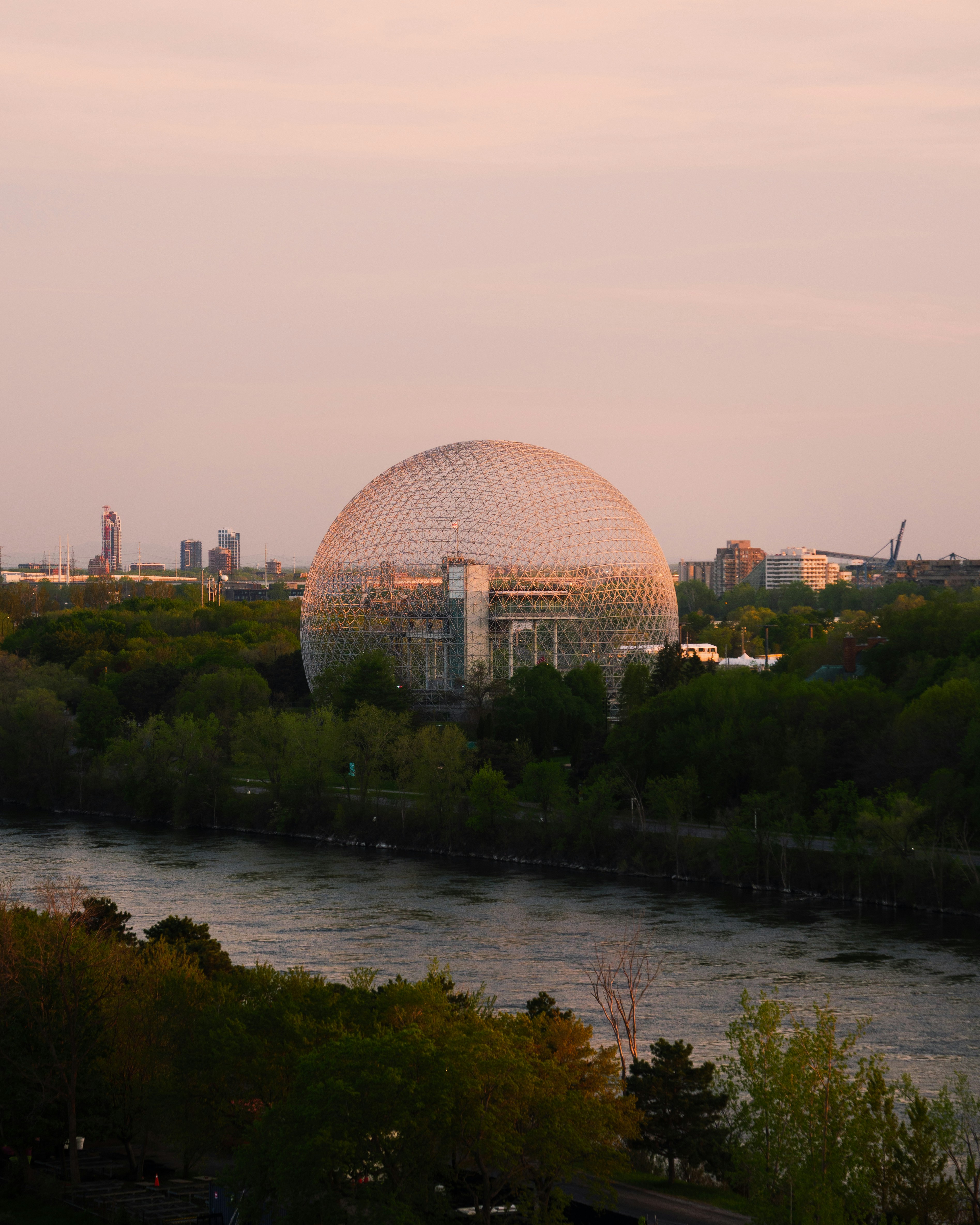 A large geodesic dome building by a river at sunset.