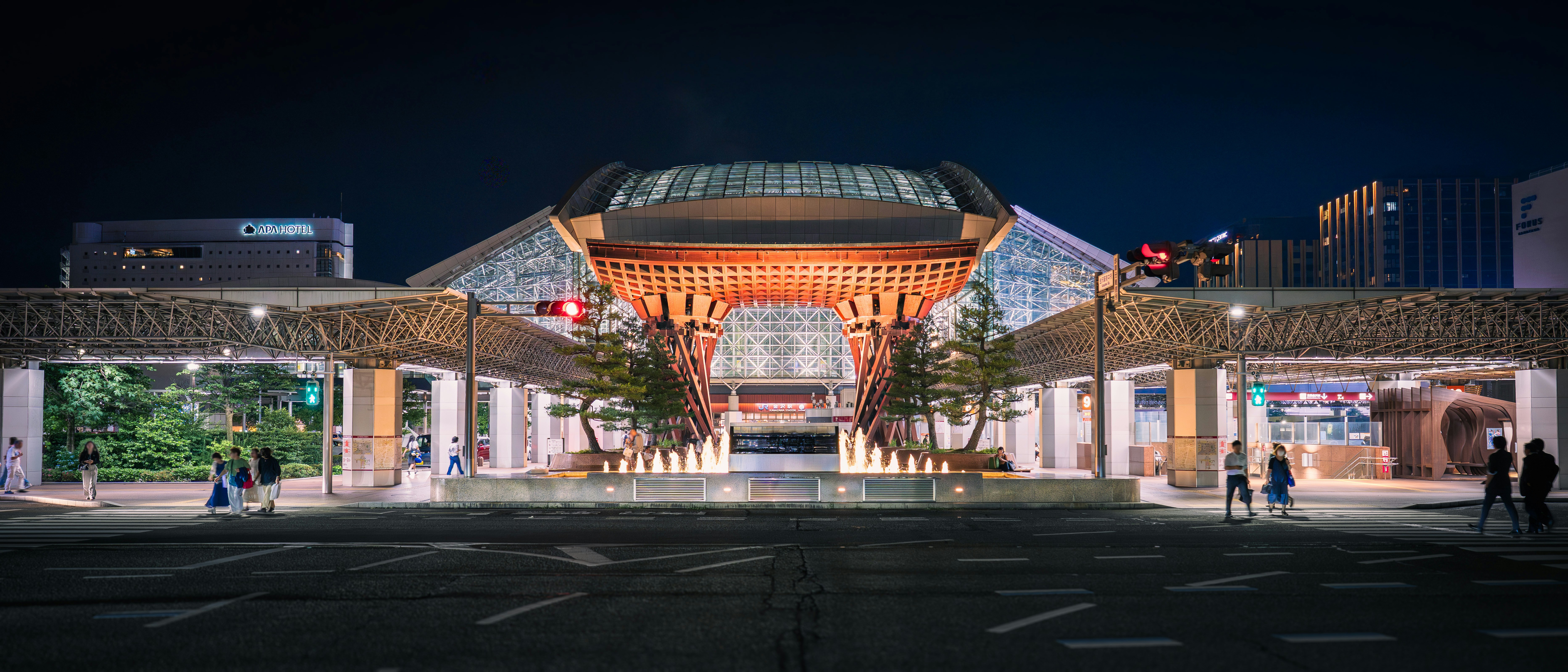 Modern illuminated building entrance at night with people walking.