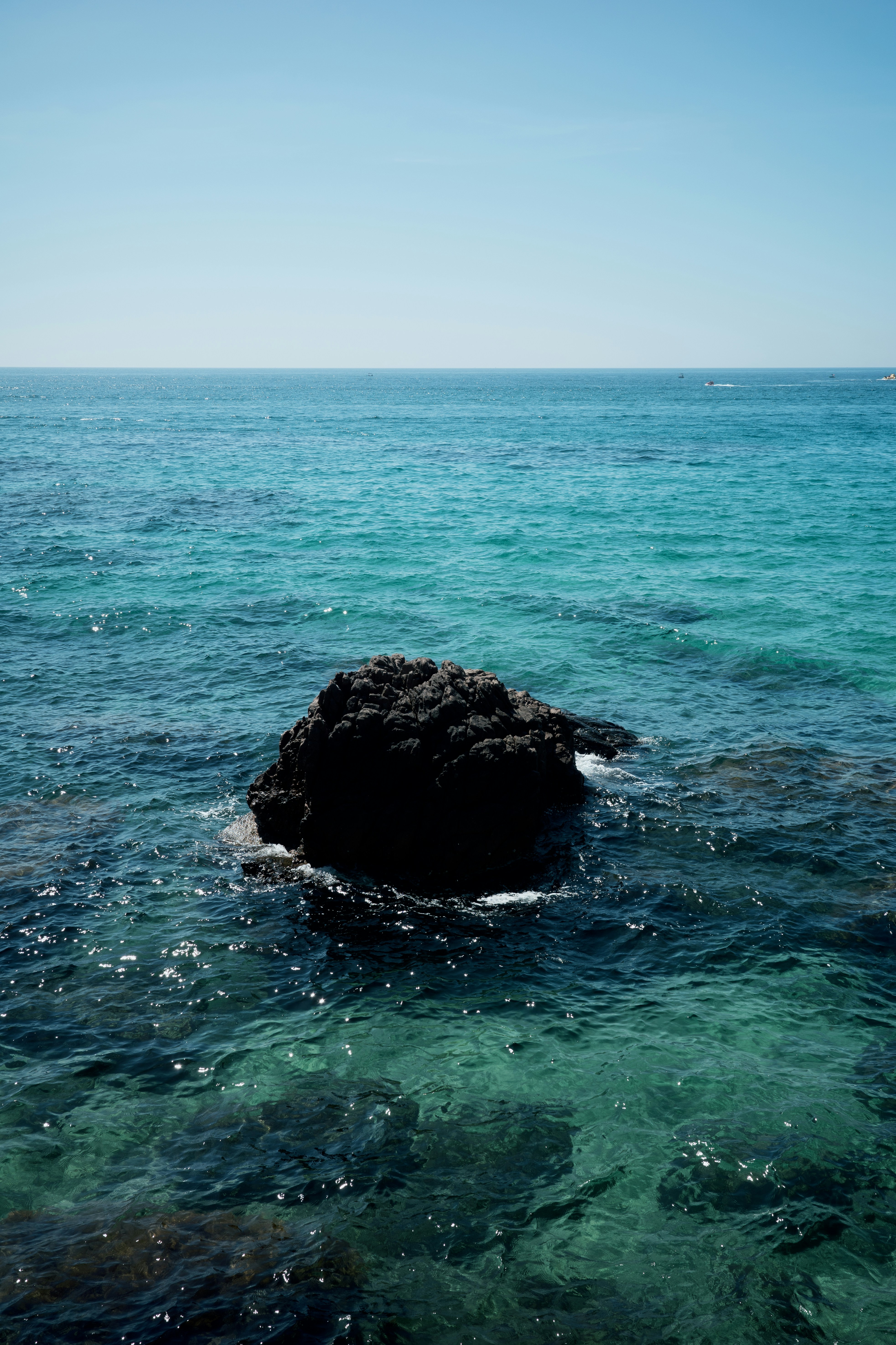 Sea Standalone: A Lone Dark Rock in Turquoise Waters Under a Clear Sky