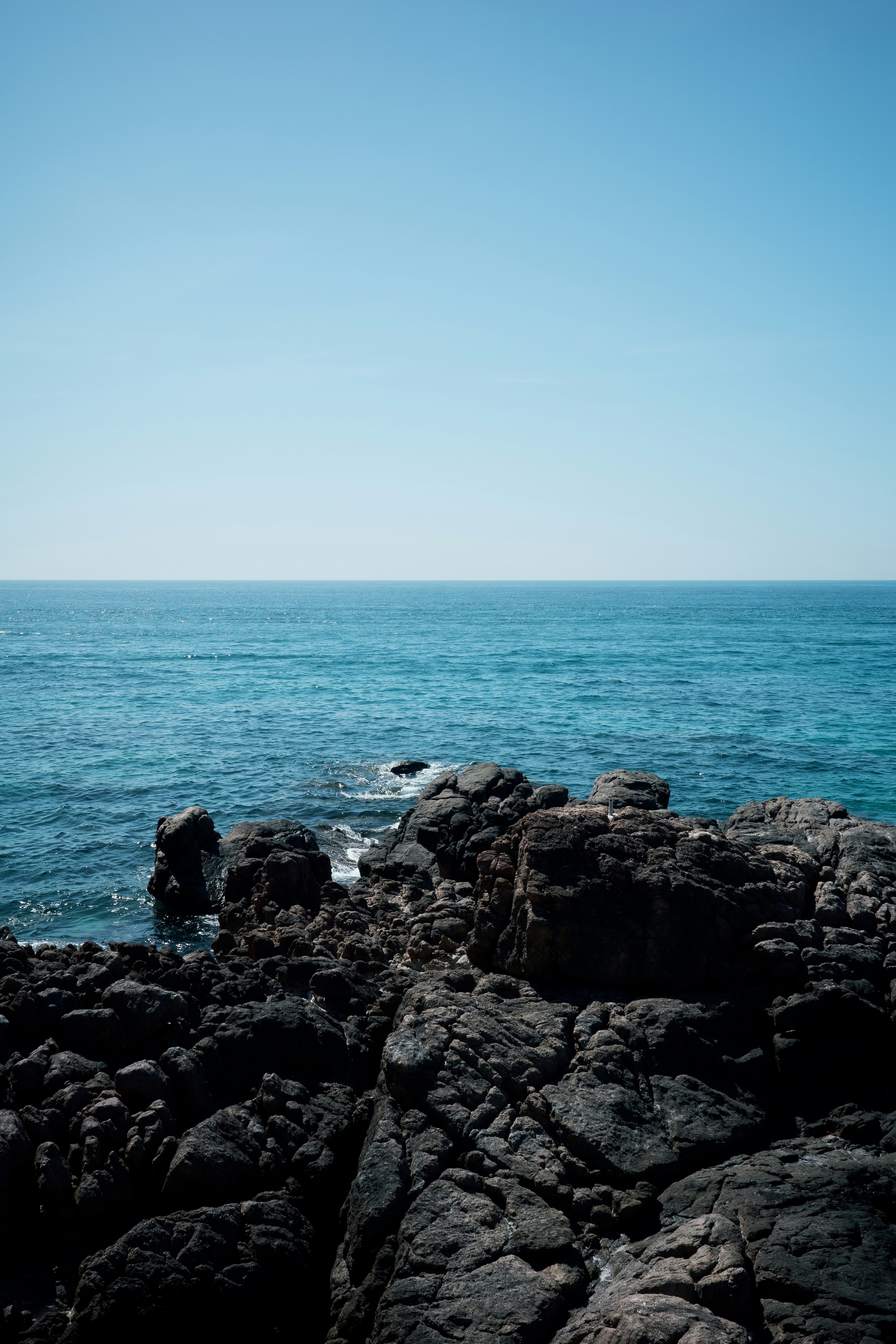 Dark coastal rocks meet the clear blue ocean and sky. photo – Free Sea ...