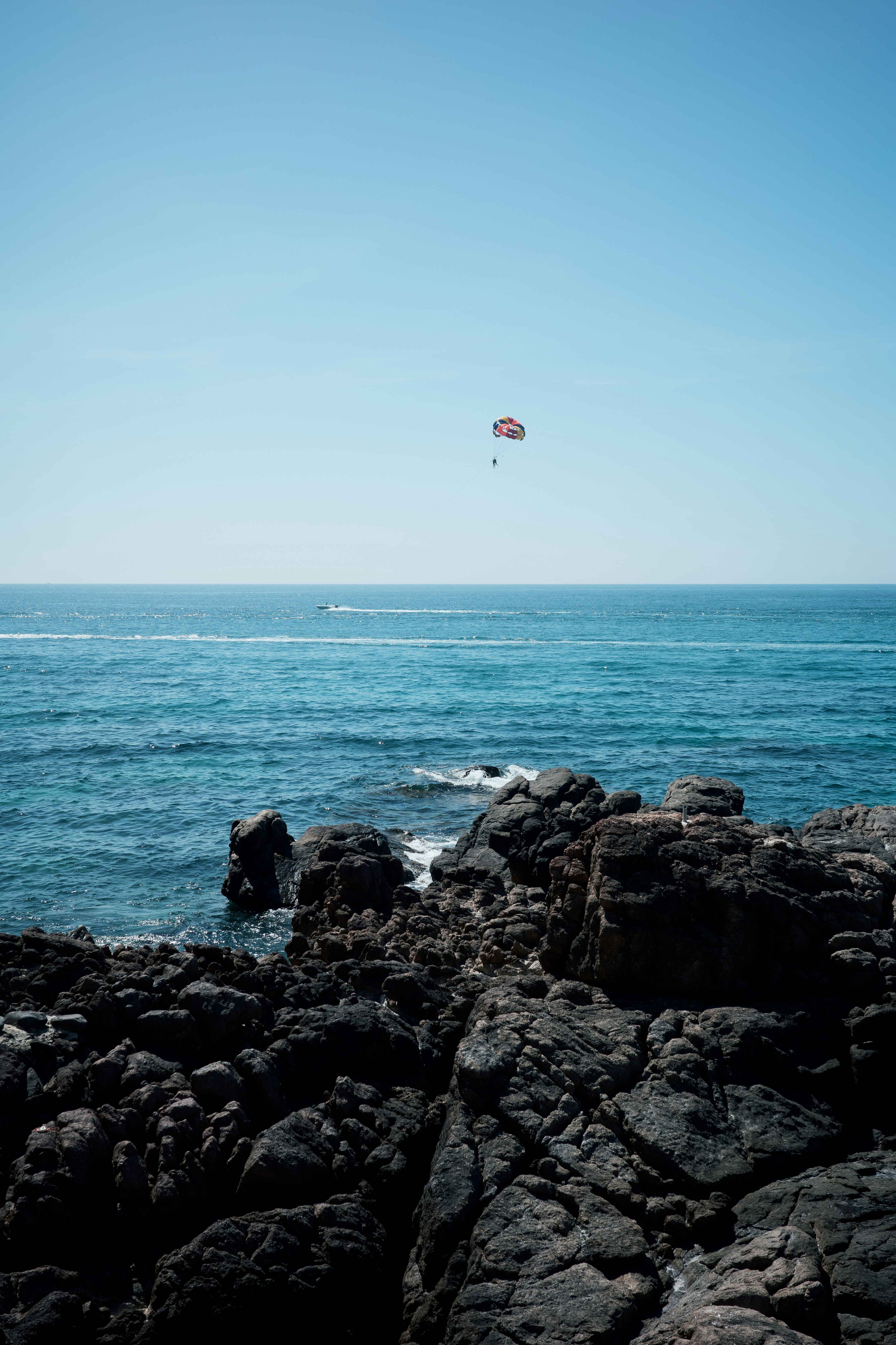 A parasailer over a rocky coastline and blue ocean.
