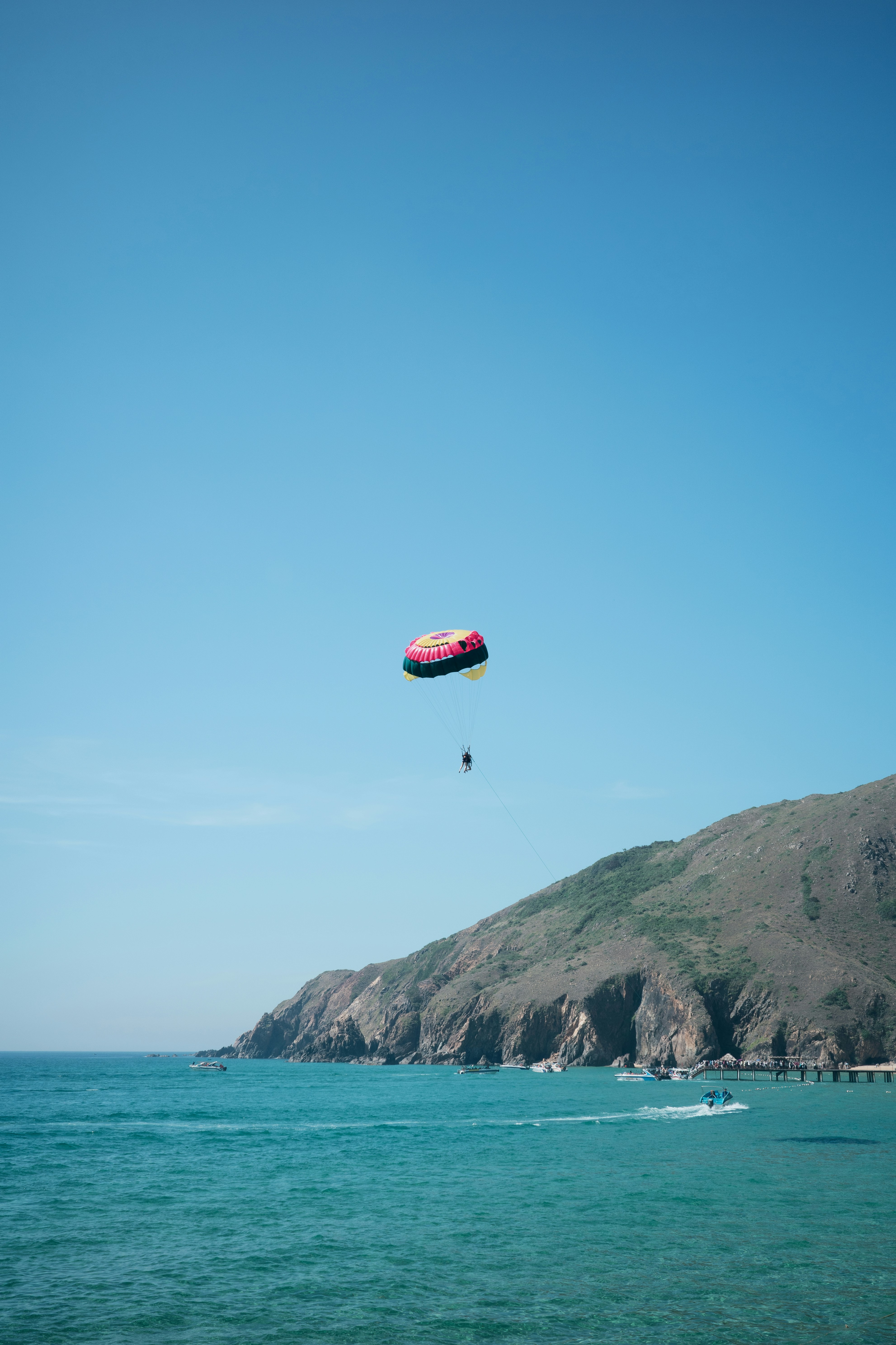 A person parasailing over turquoise water near a green mountain.