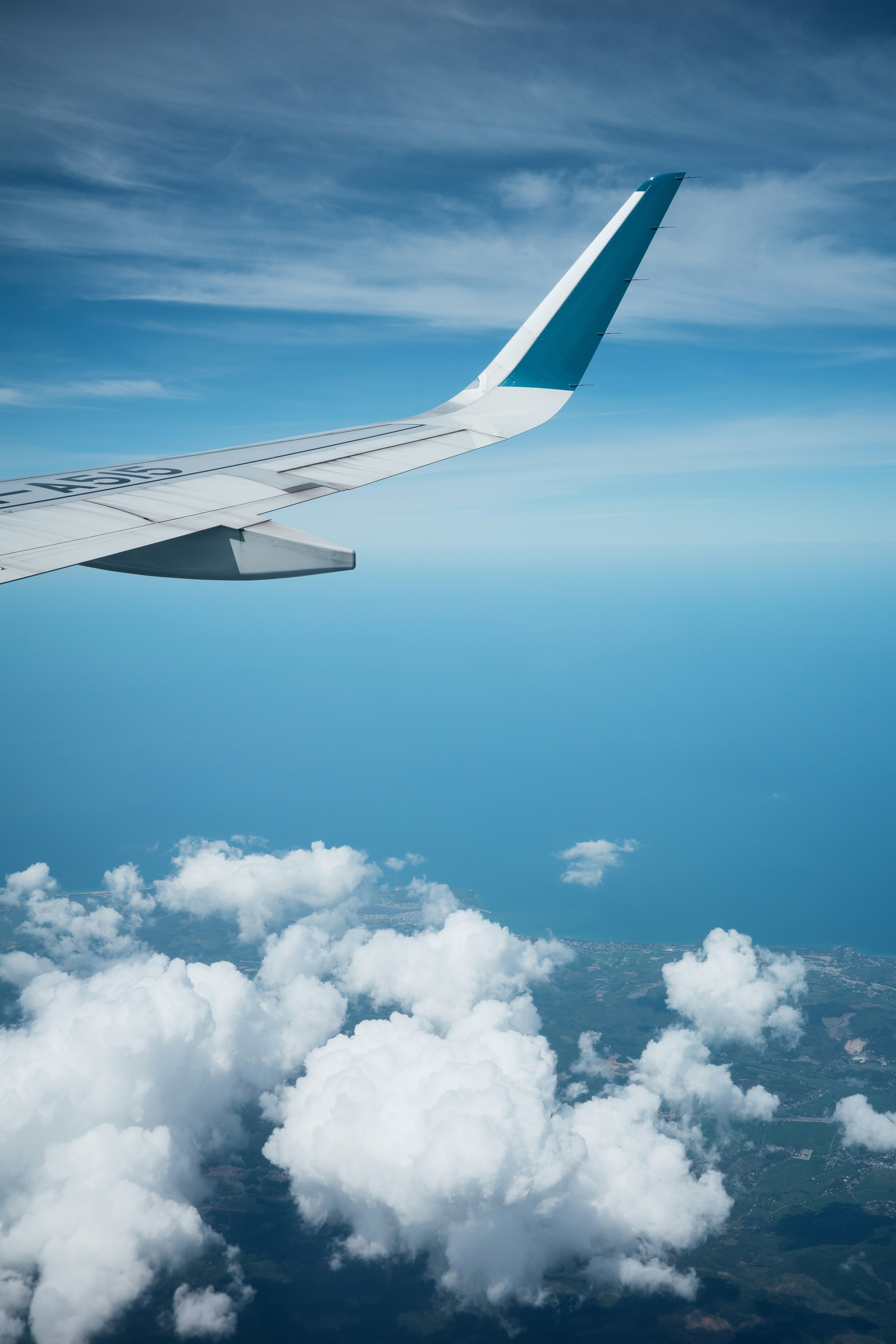 Airplane wing above clouds, land, and a vast blue sea.