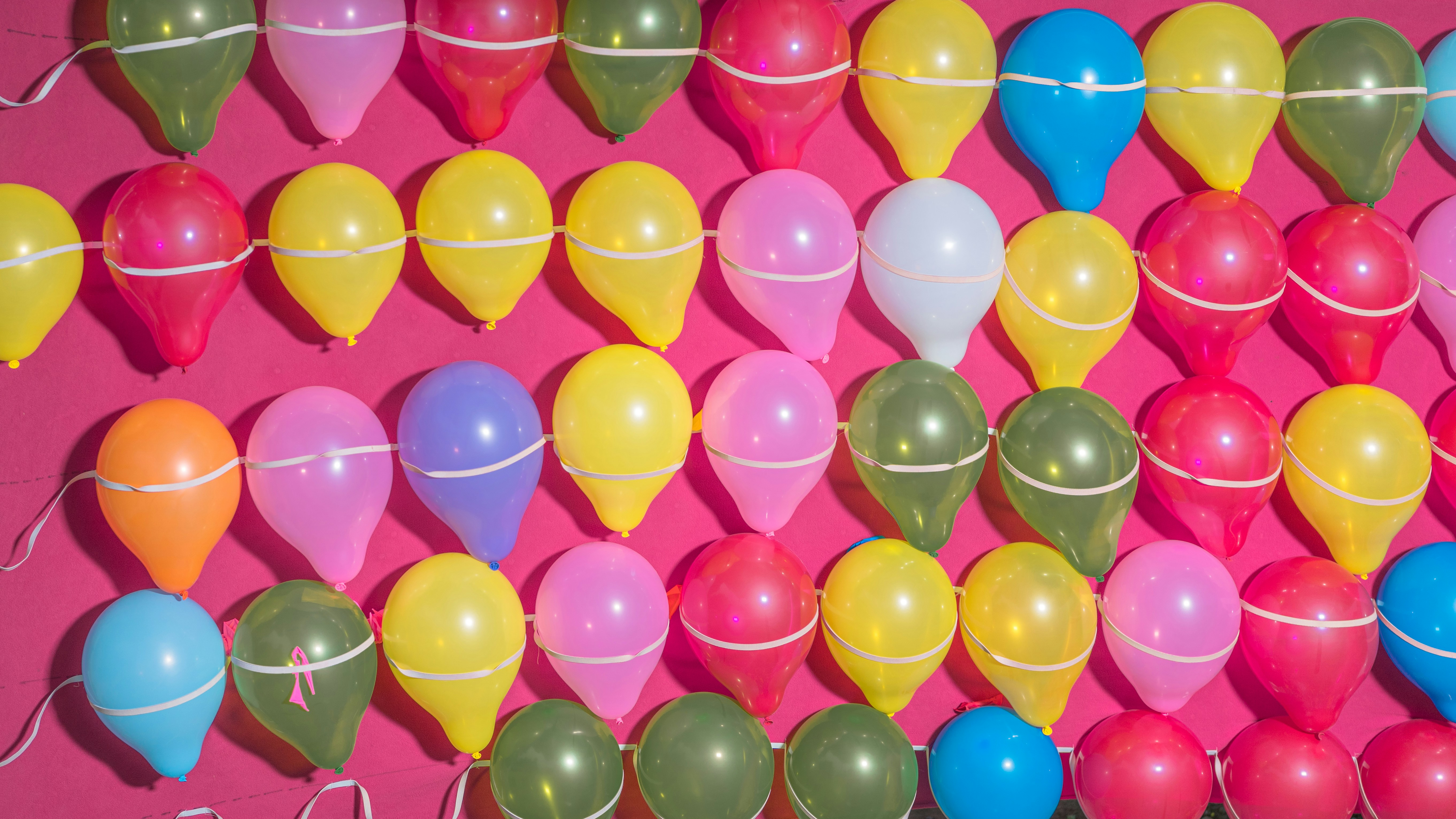 Rows of colorful balloons against a vibrant pink background.