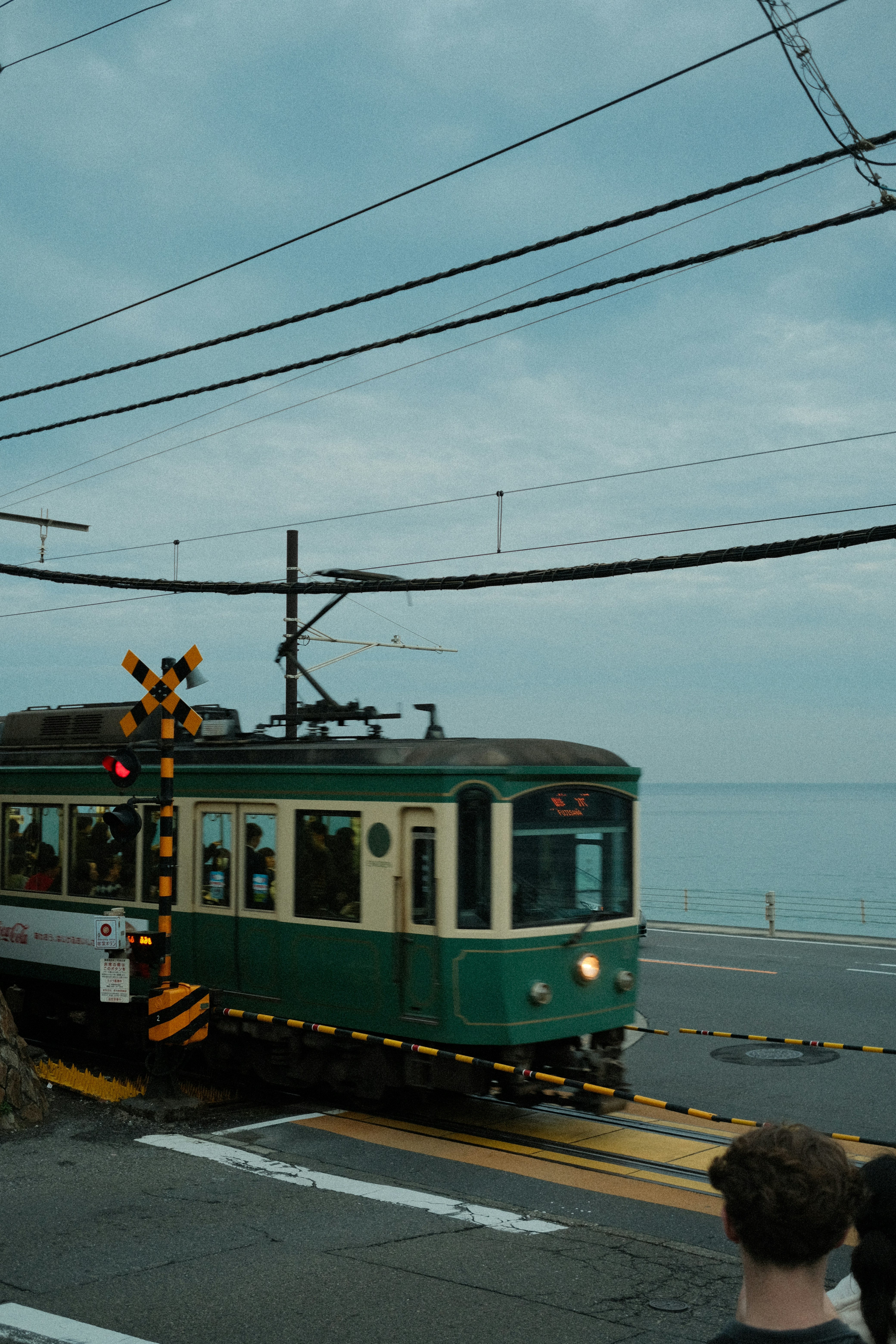 Green train crossing tracks near ocean under cloudy sky.