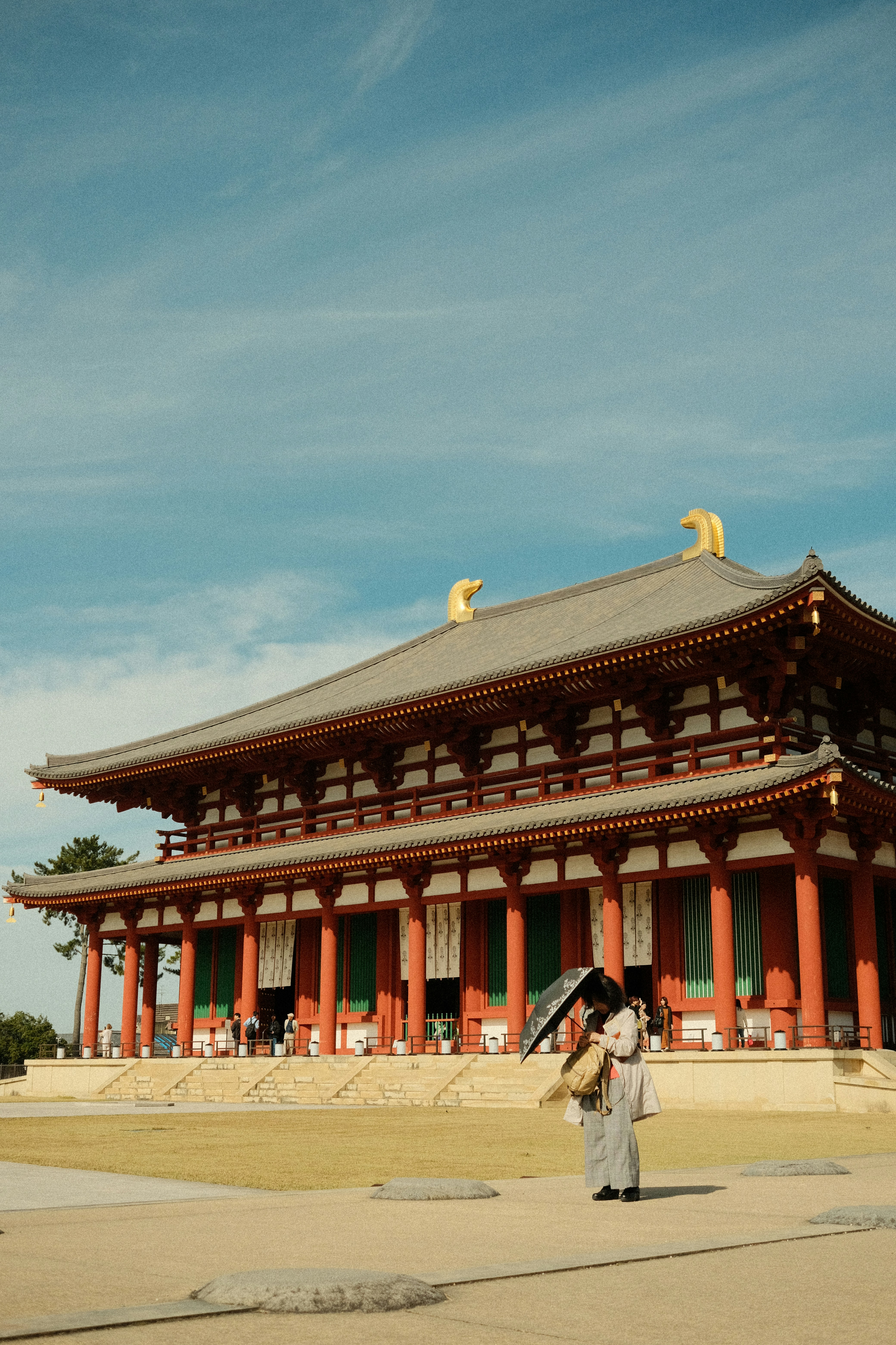 A traditional red-brick temple with a person in traditional attire stands in a sunlit courtyard, capturing a calm, historic scene.
