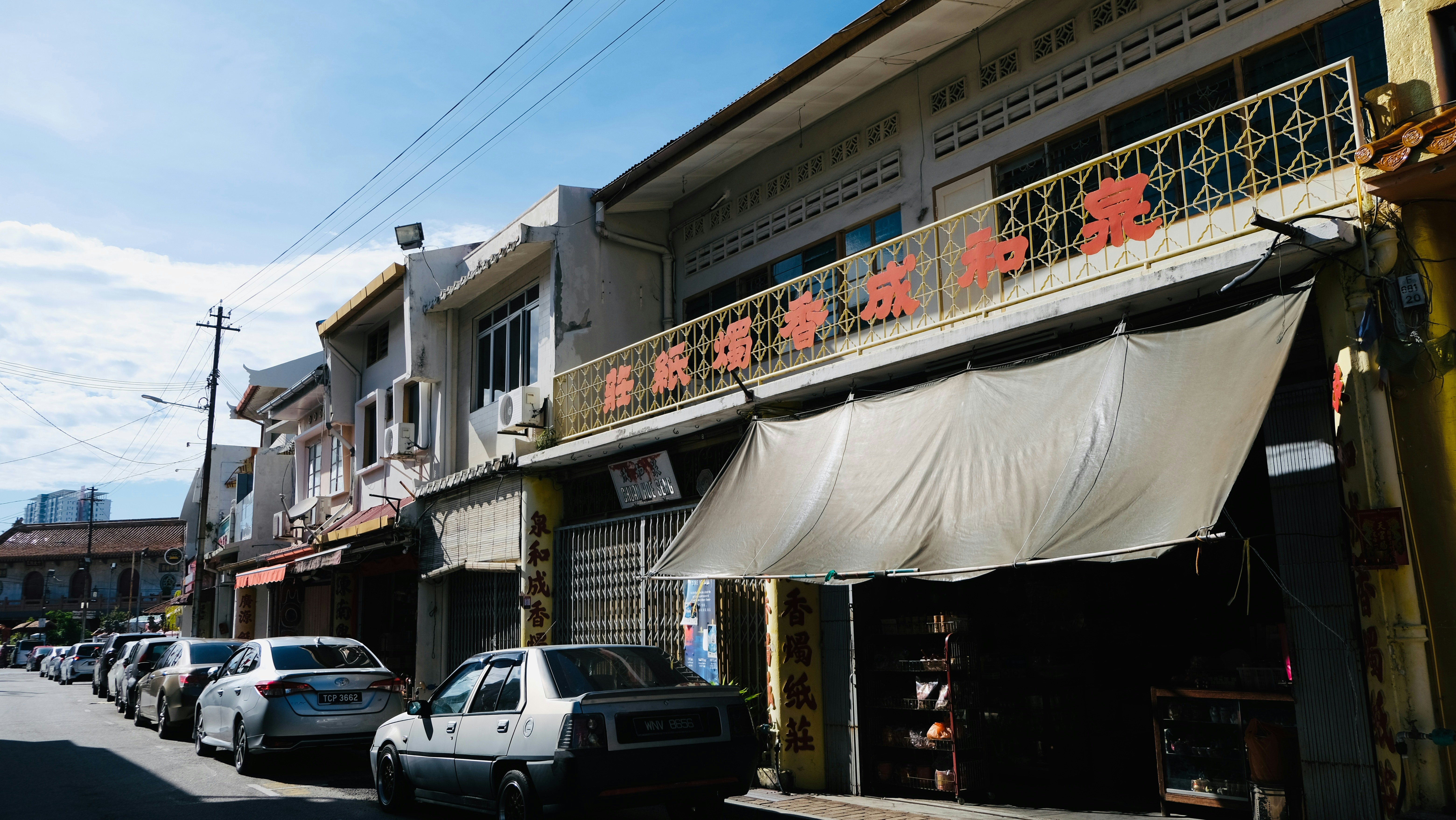 Shaded Market Facade: A Quiet Street of Shopfronts and Cars