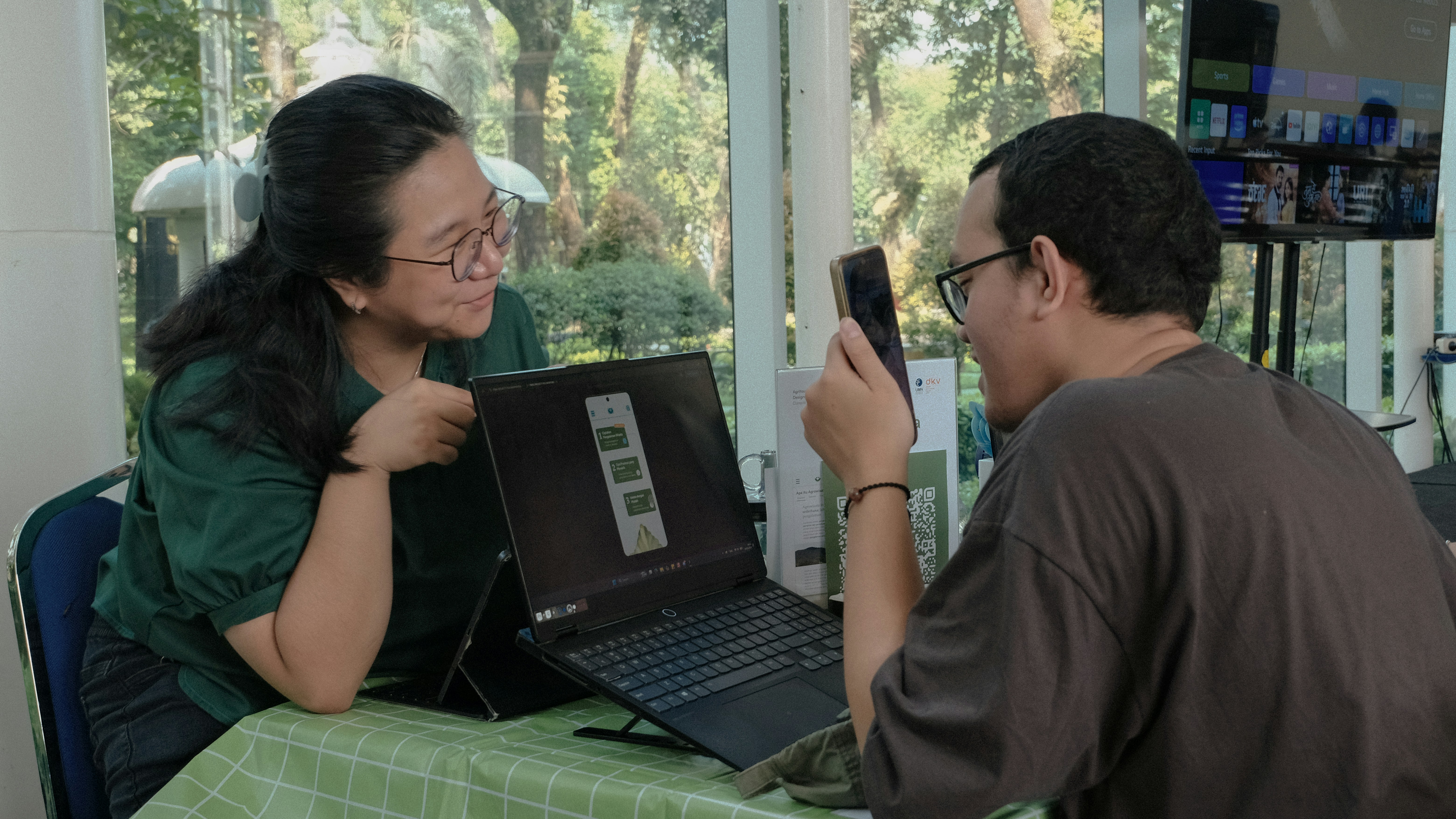 Man scanning laptop screen with phone, woman watching.