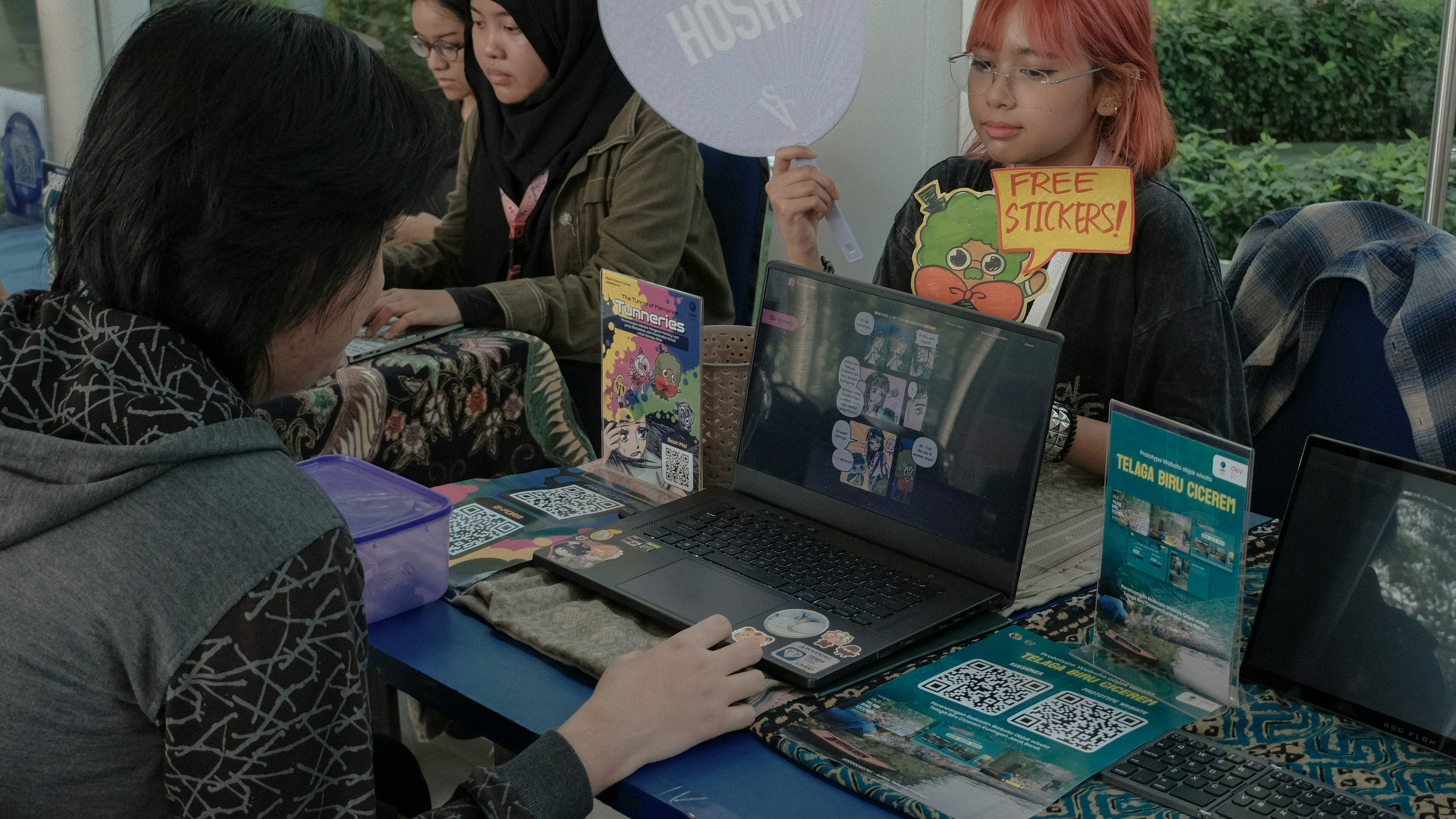 People interacting at an outdoor stall with a laptop display.