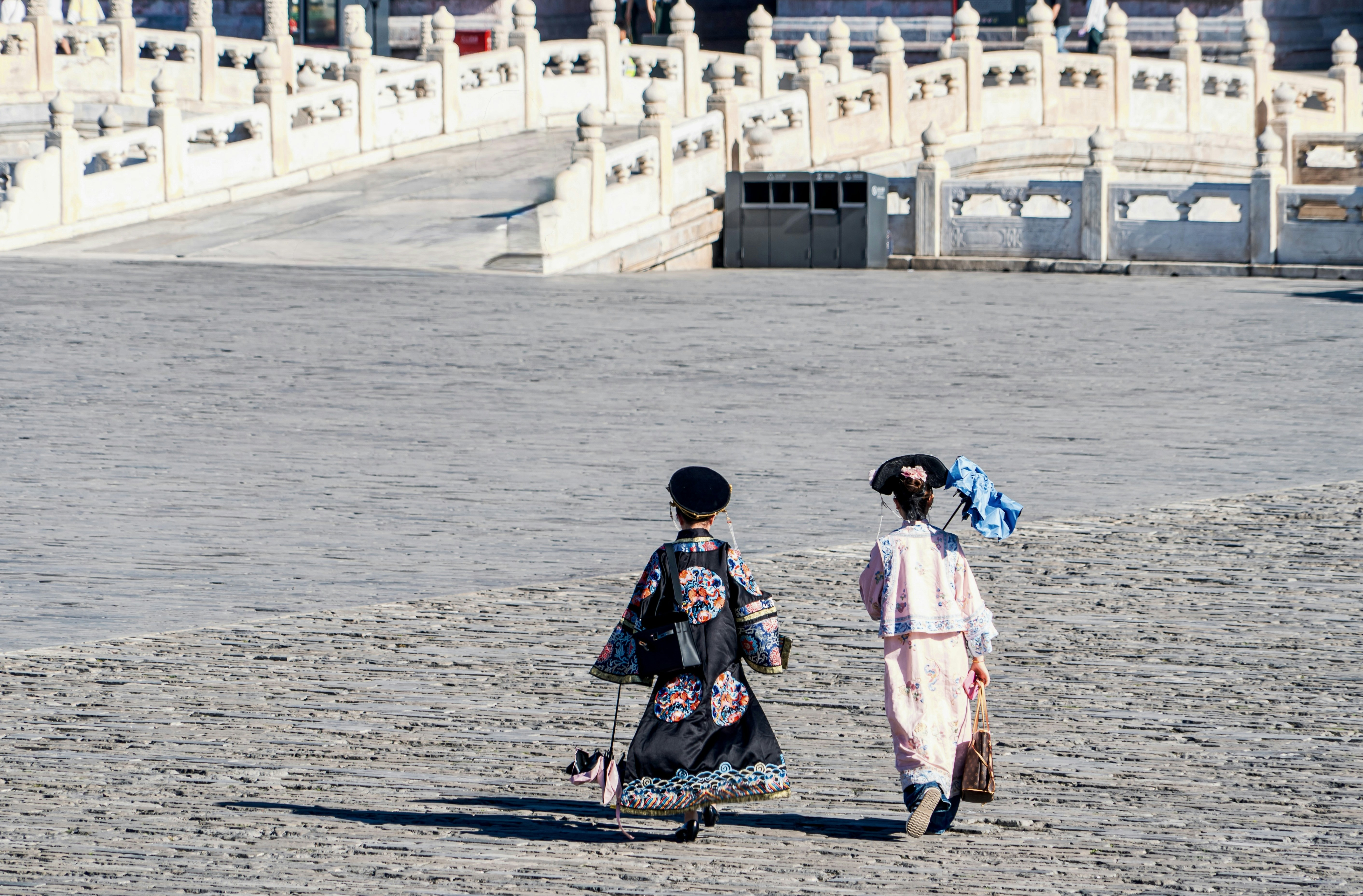 Two people in traditional attire walk past a stone bridge.