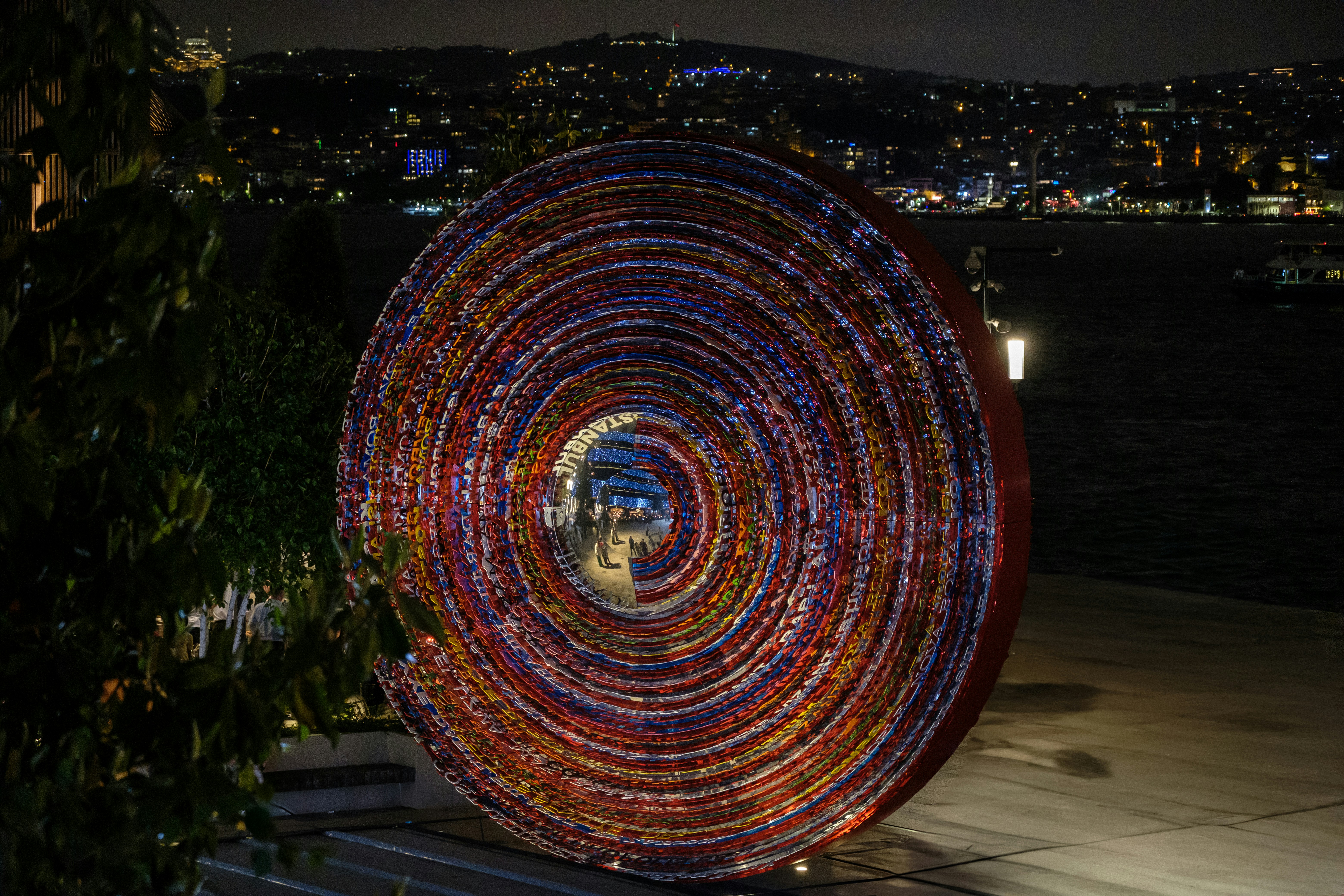 Circular Night Art: A Kaleidoscopic Wheel by the Water