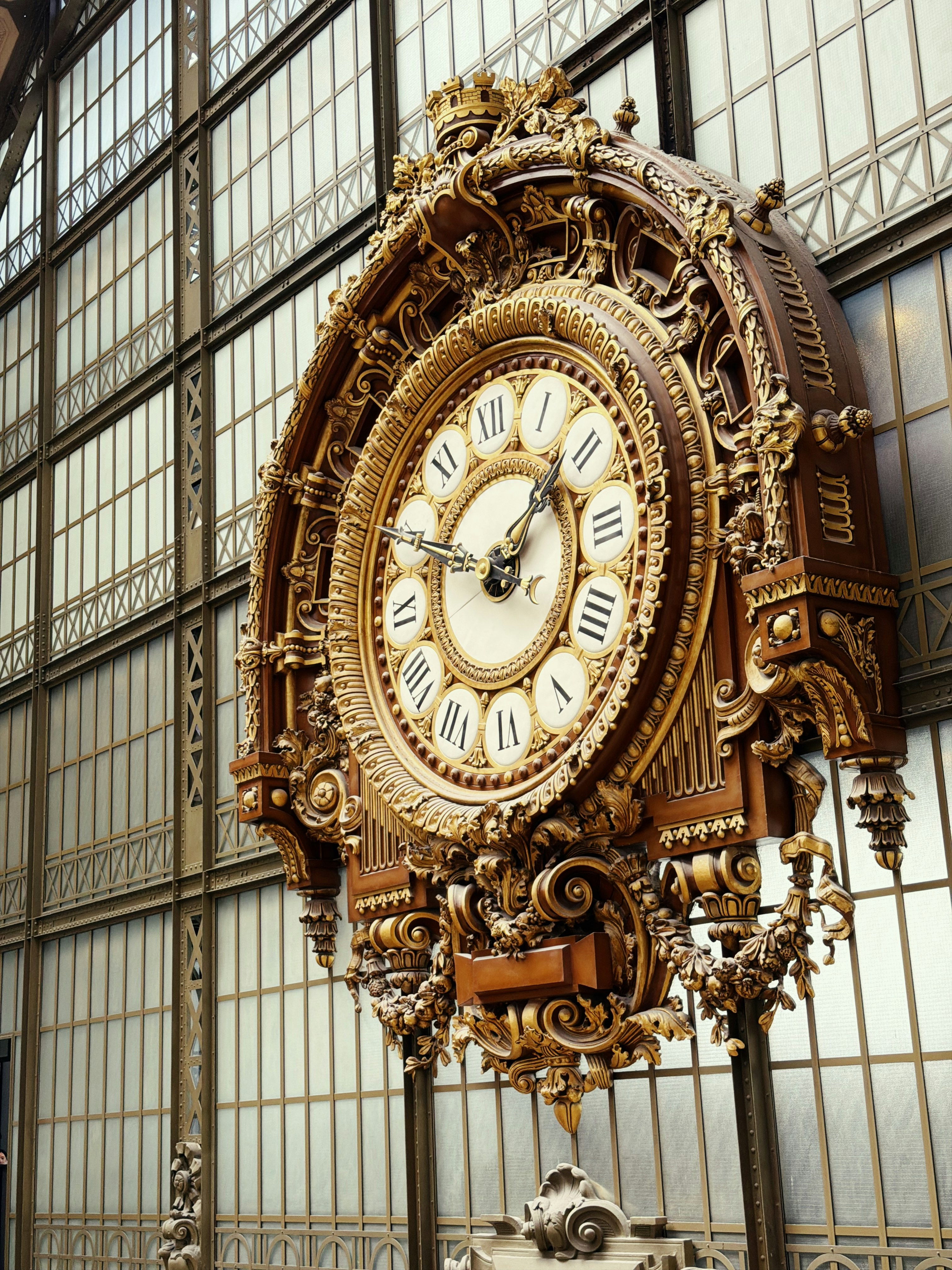 Ornate Clock Crown: A Golden Timepiece Within Glass and Steel Framing