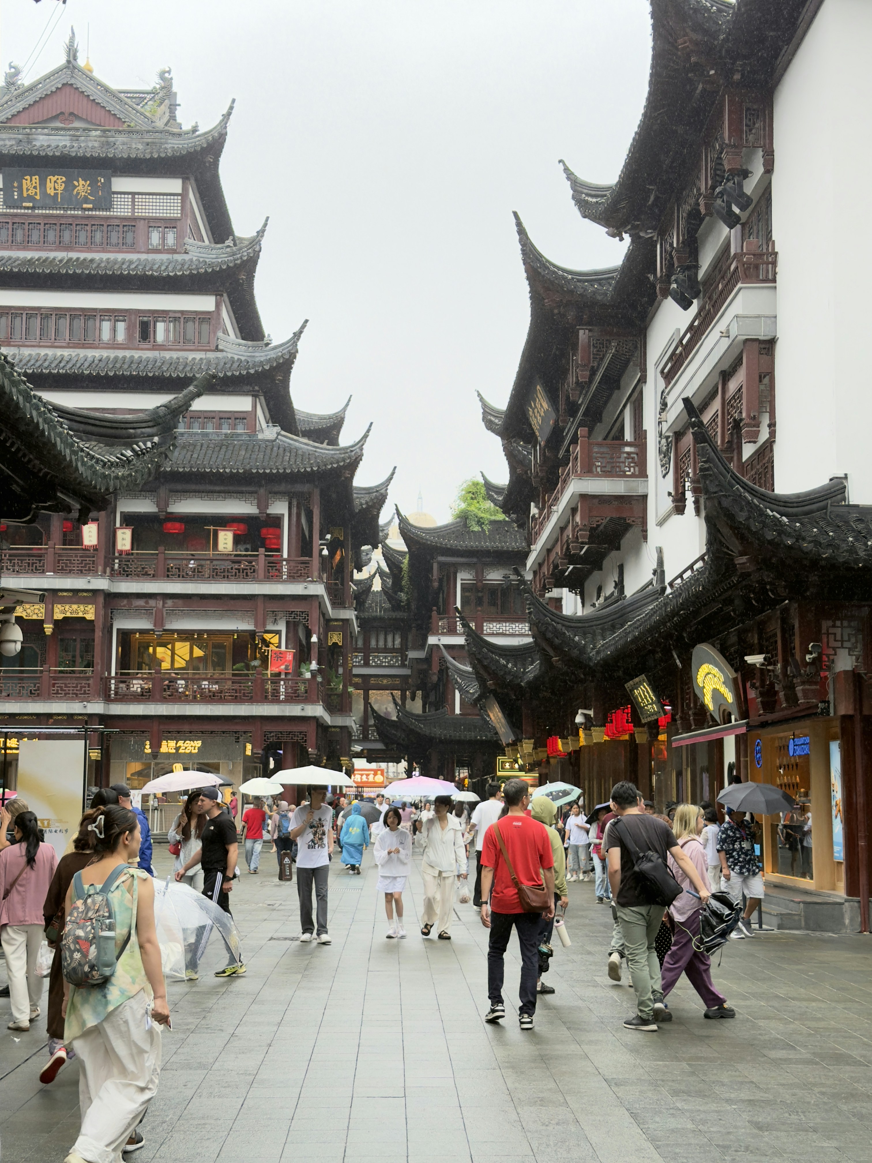 Visitors gather in front of ornate traditional Chinese pavilions with sweeping tiled roofs at a busy old-town market in Shanghai.