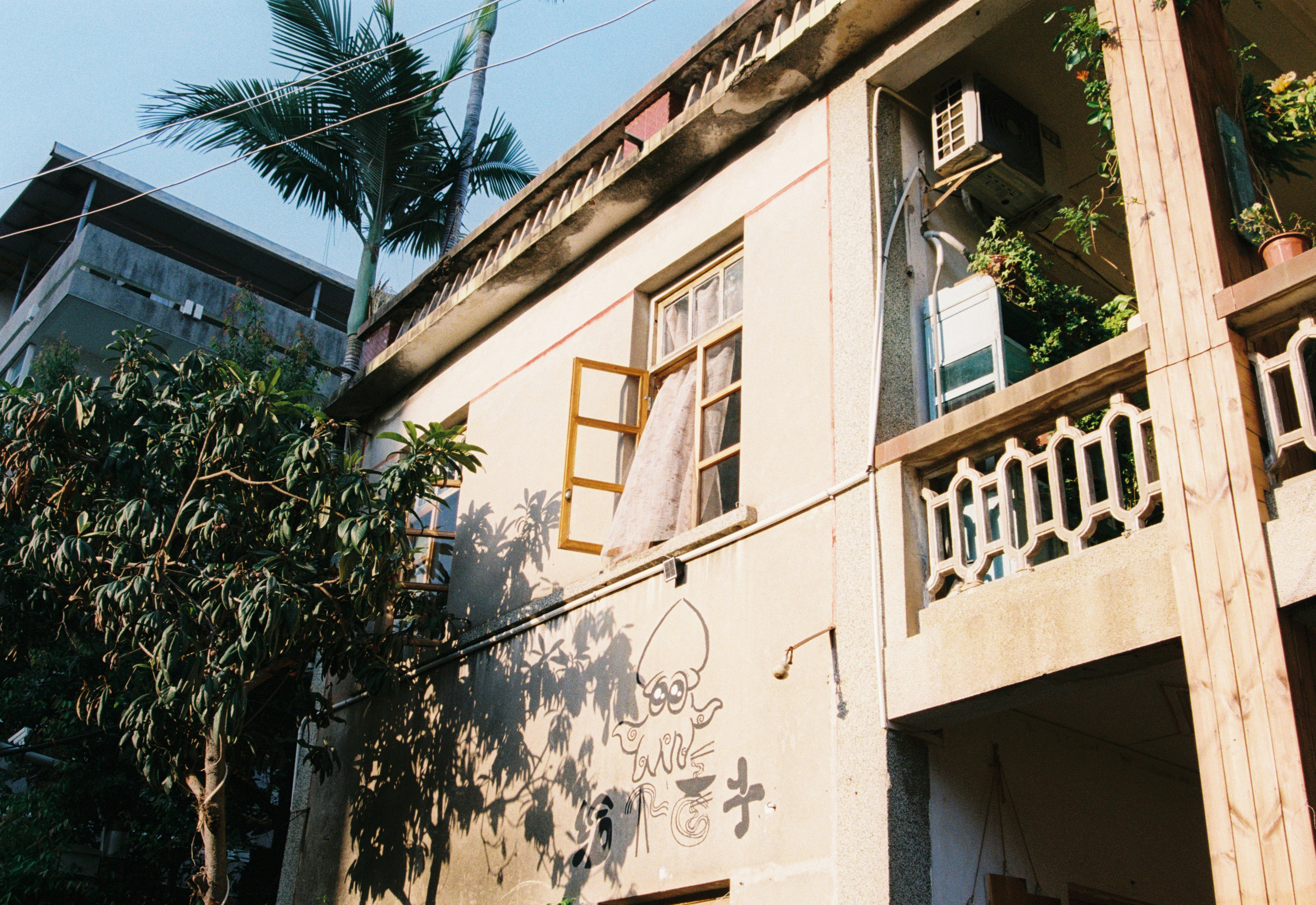 Sun-drenched building facade with a small balcony and a playful mural on the wall; a scene suggesting a lived-in urban residence.