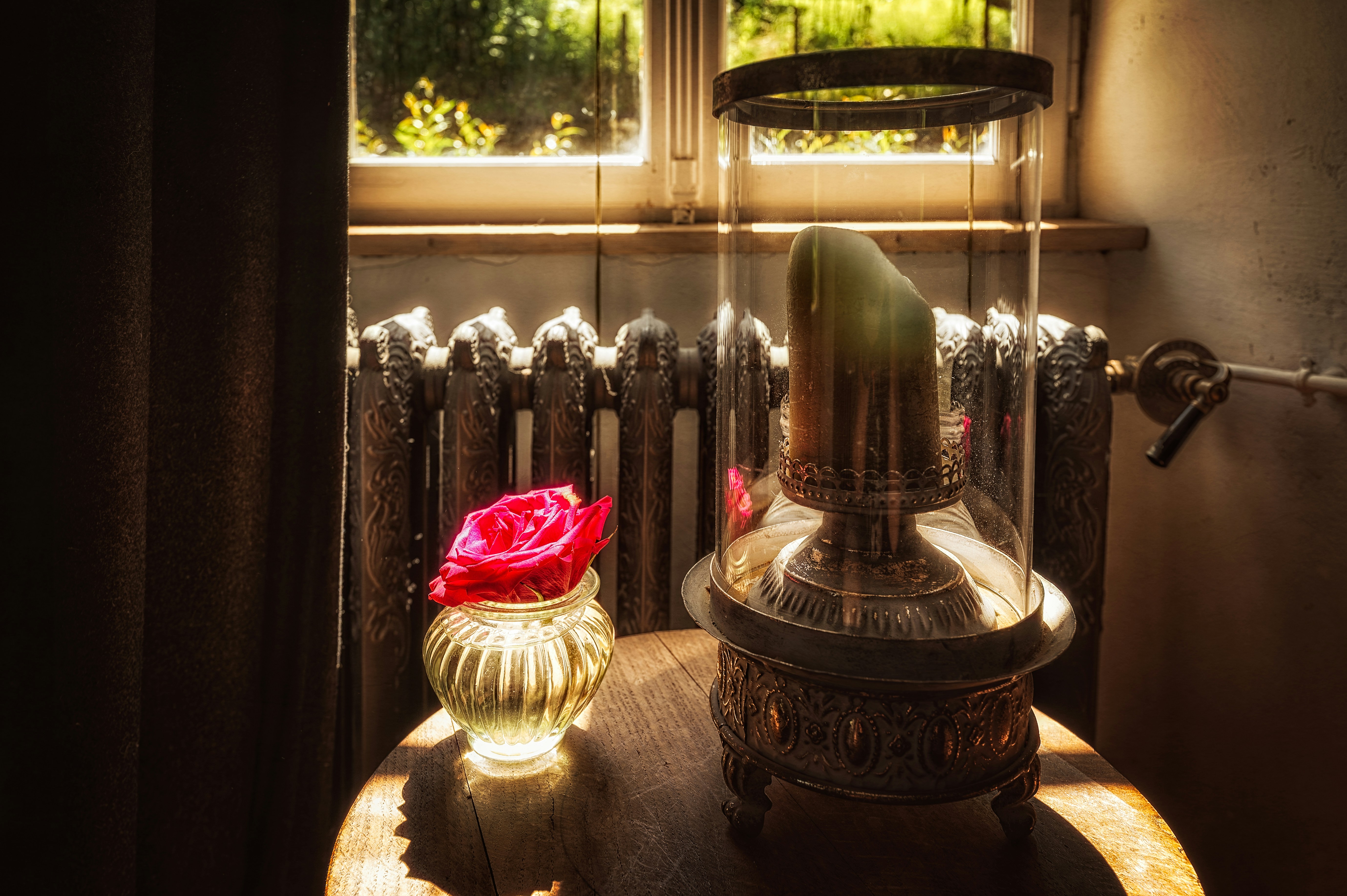 A red rose and candle by a sunlit window.