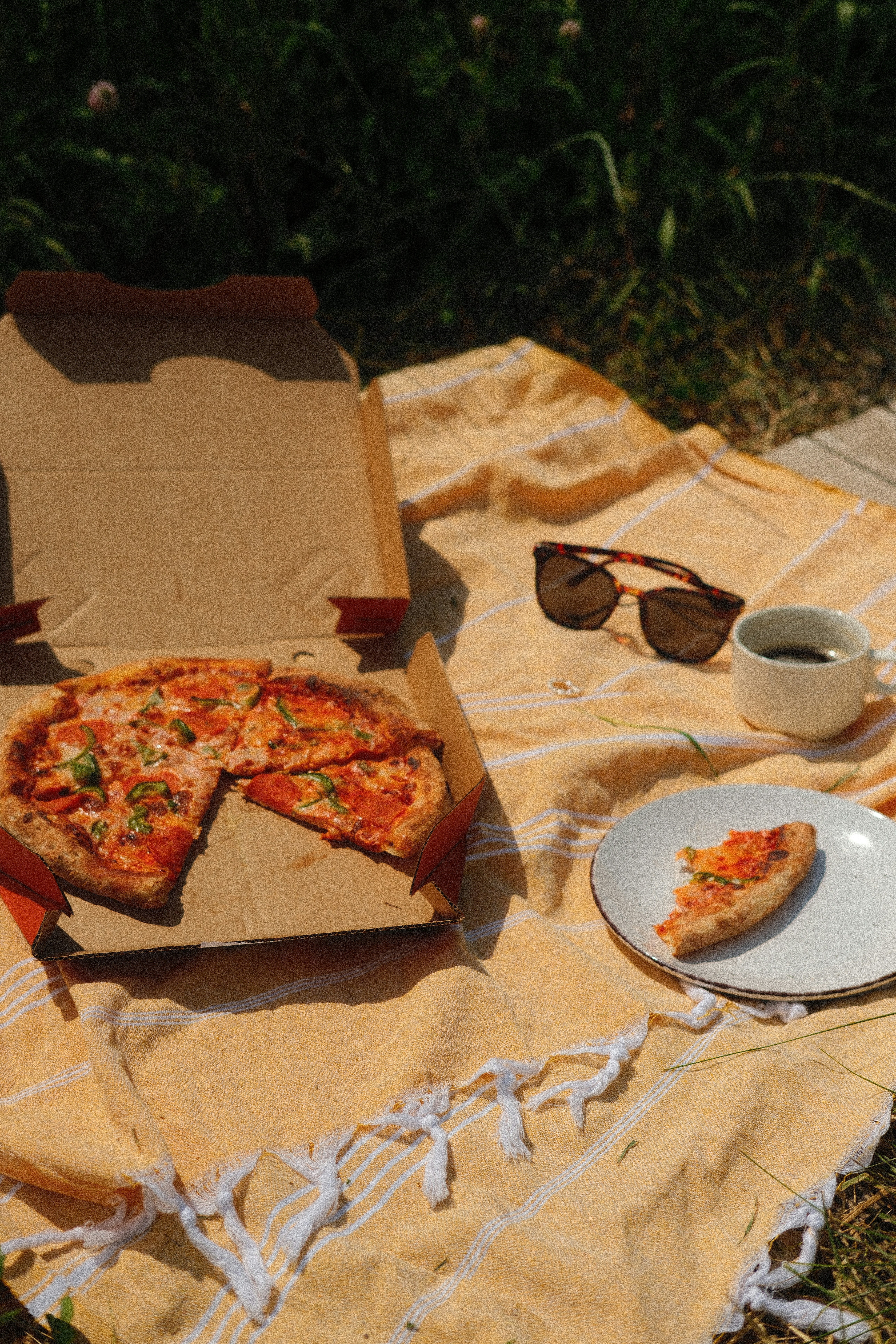 Pizza picnic on a yellow blanket with coffee and sunglasses.