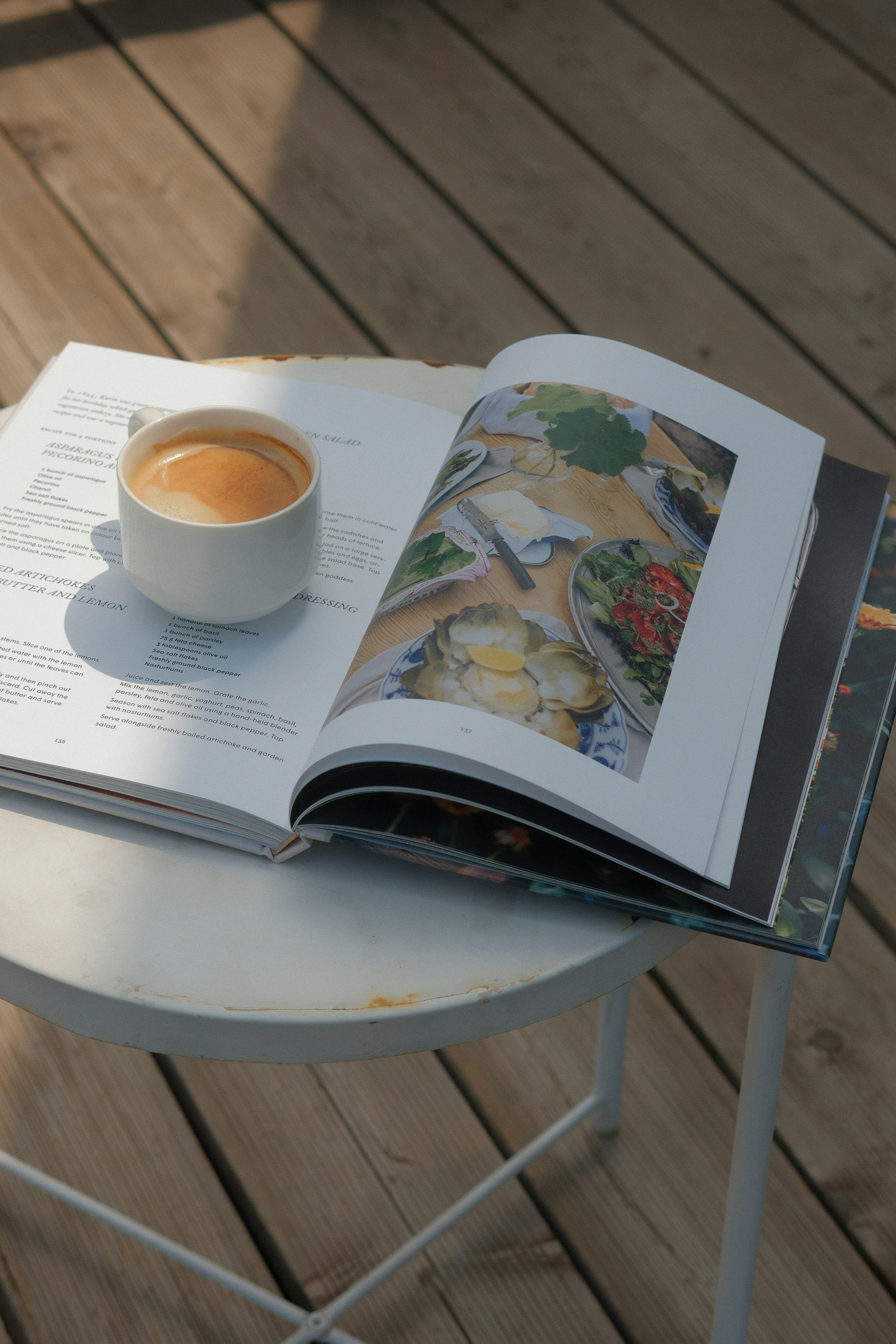 Coffee and cookbook on a white table outdoors.