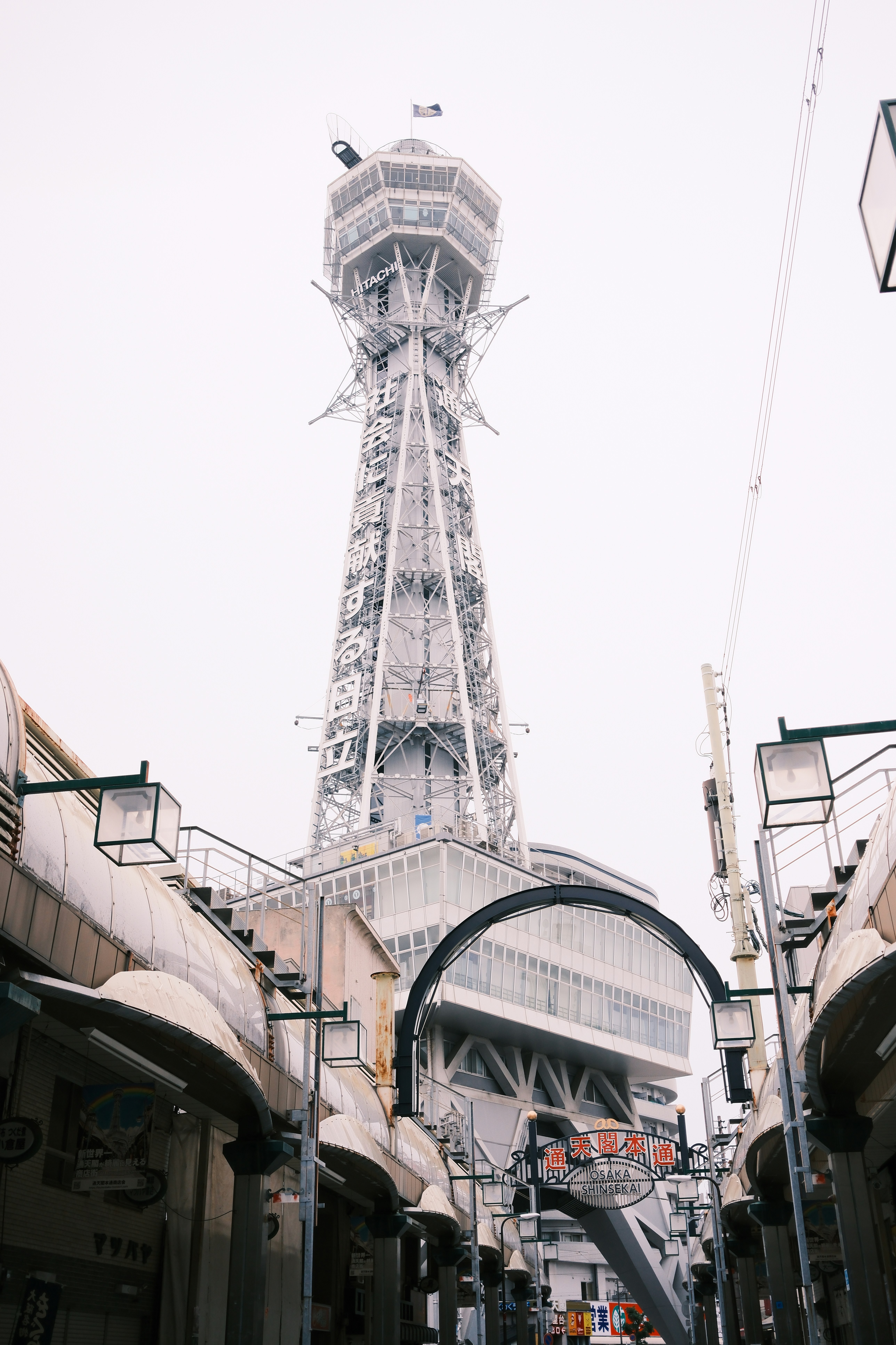 Tokyo Tower rises above a bustling arcade lined with lanterns and signage