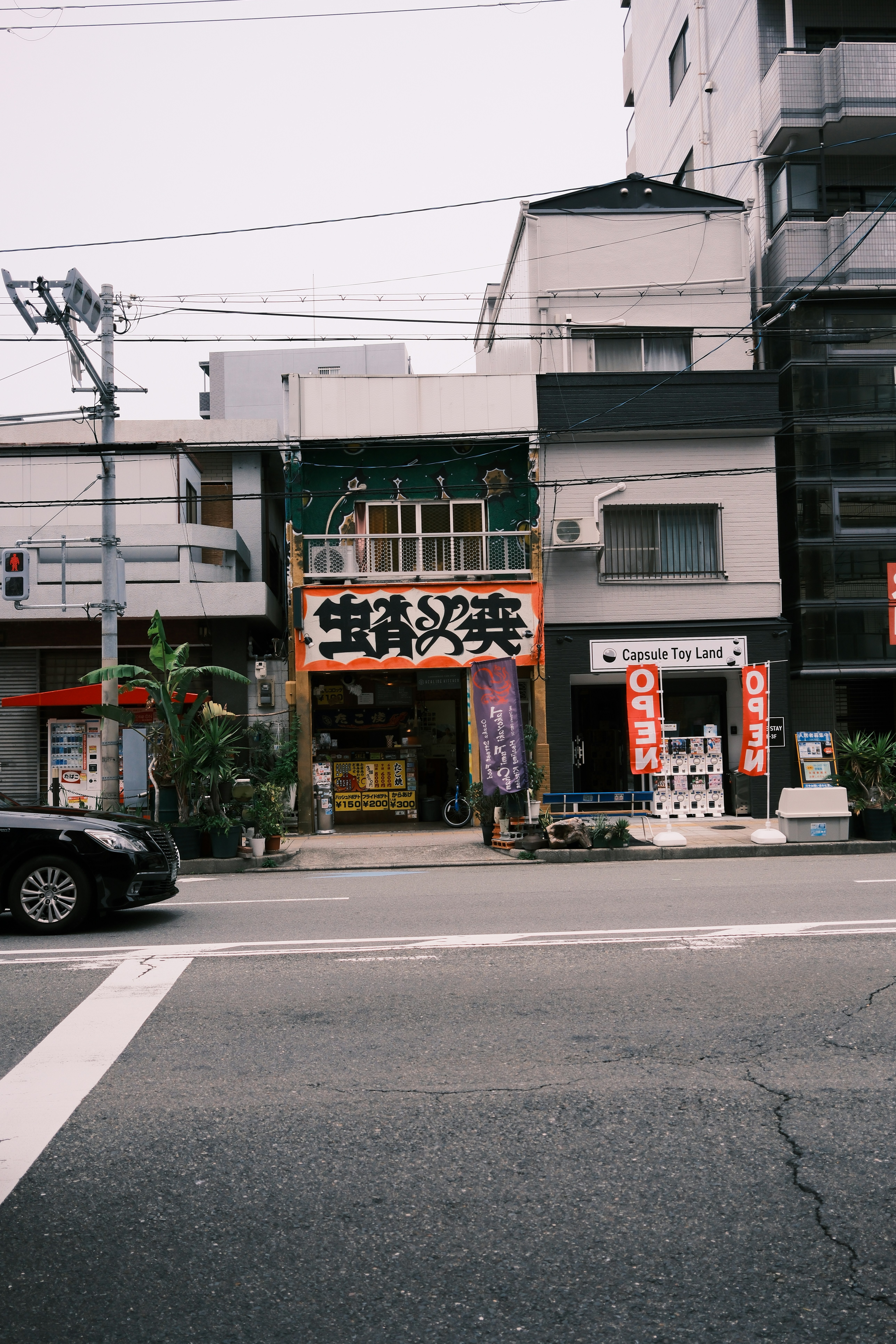 Overcast urban street with buildings, signs, and a car.