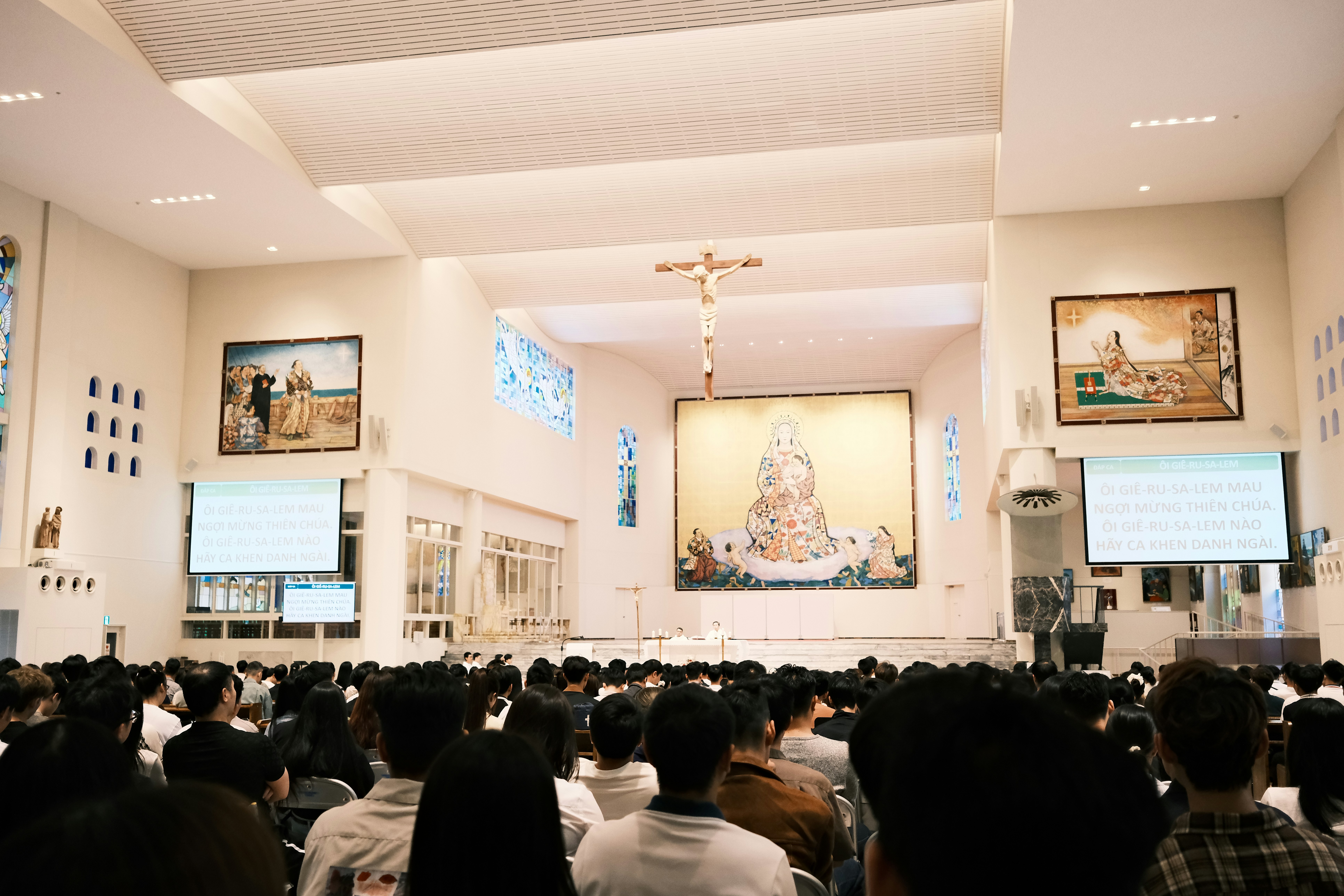 Congregation seated in a spacious church with religious artwork.