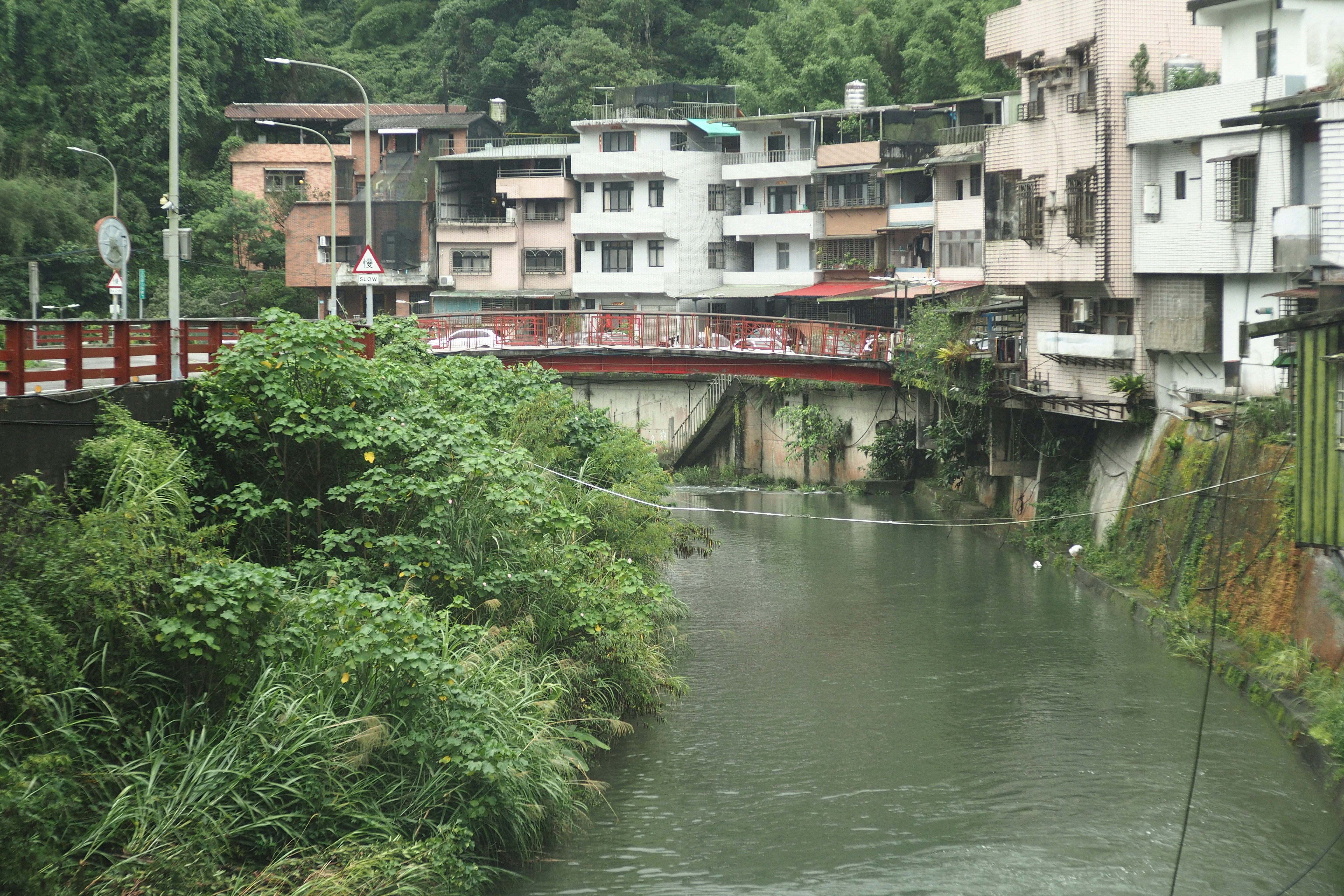 Red Bridge Over Quiet Riverbend Between Whitewashed Buildings