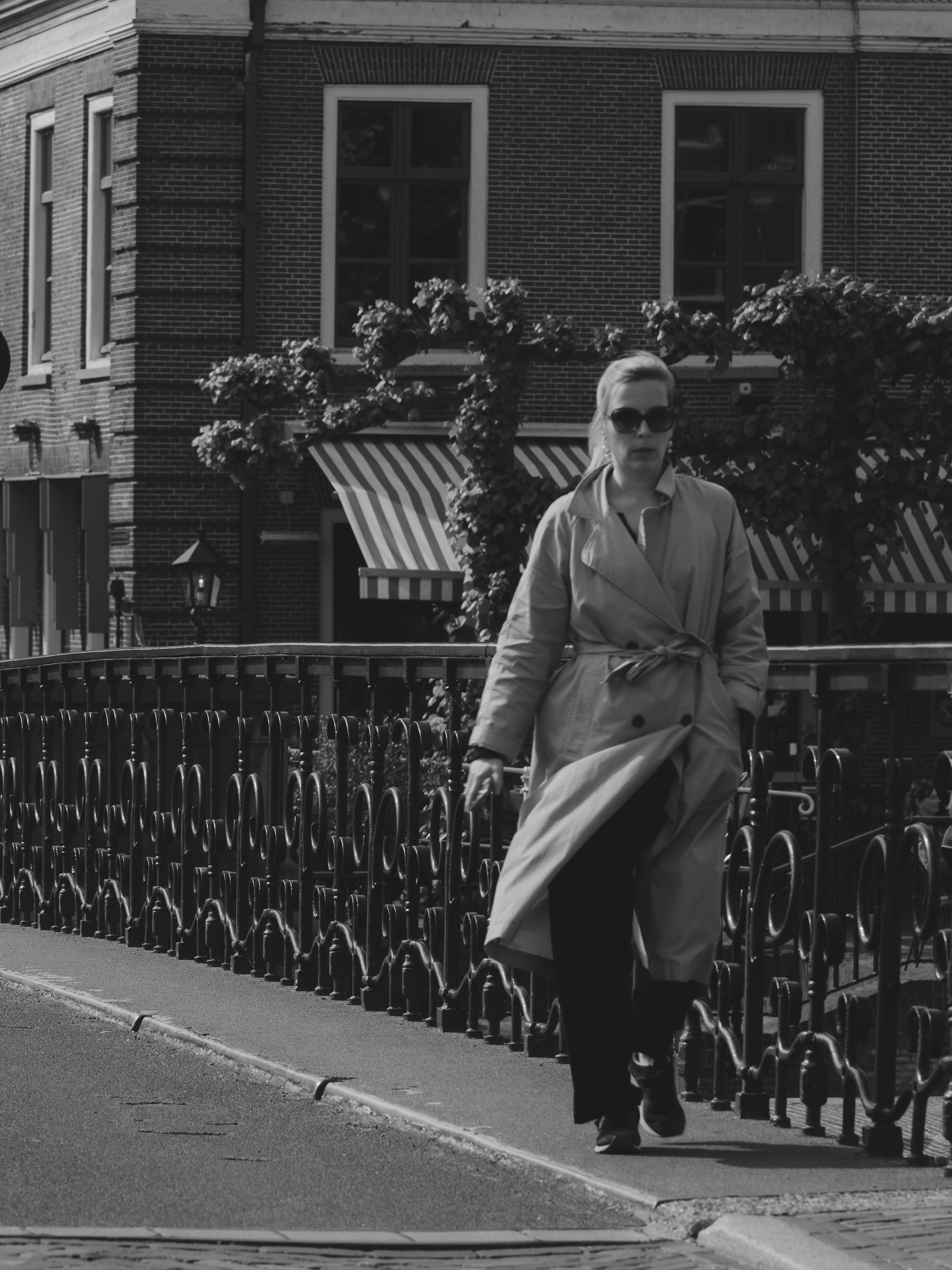 Trench-coat stride along a sunlit city bridge