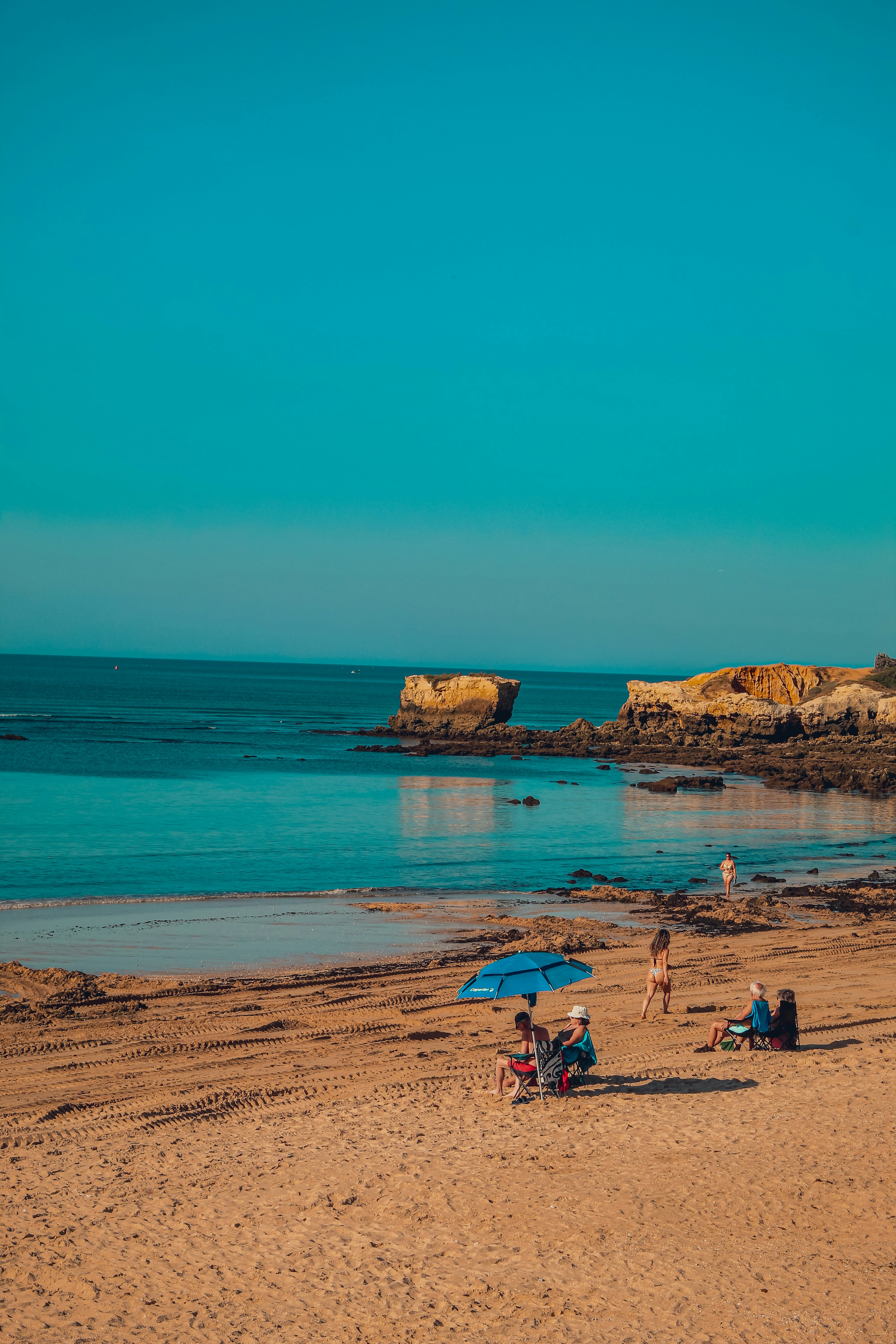 Coastal Repose: Sunlit Beach with People under a Blue Canopy