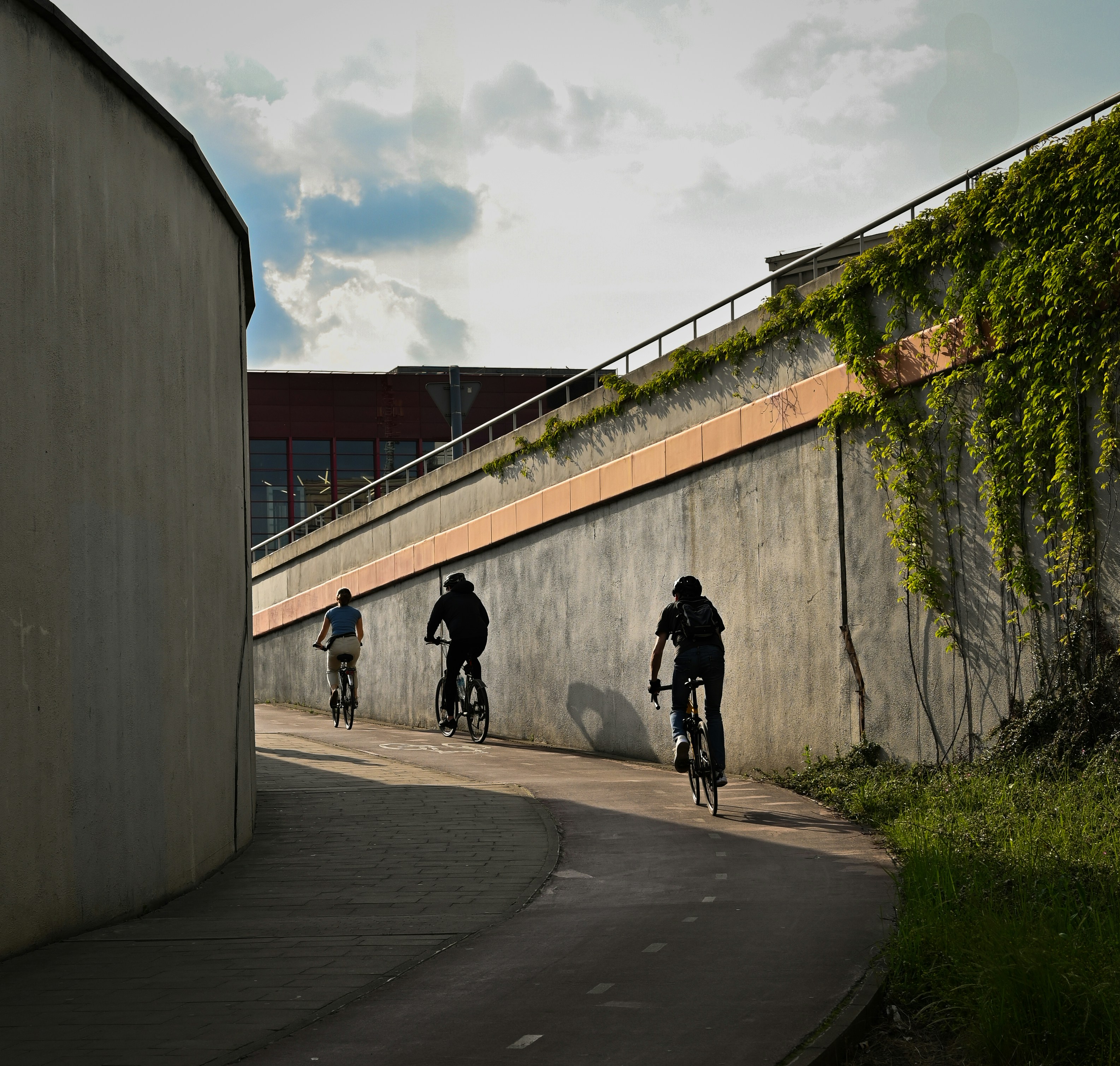 Three cyclists riding up a bike path between concrete walls in a city underpass