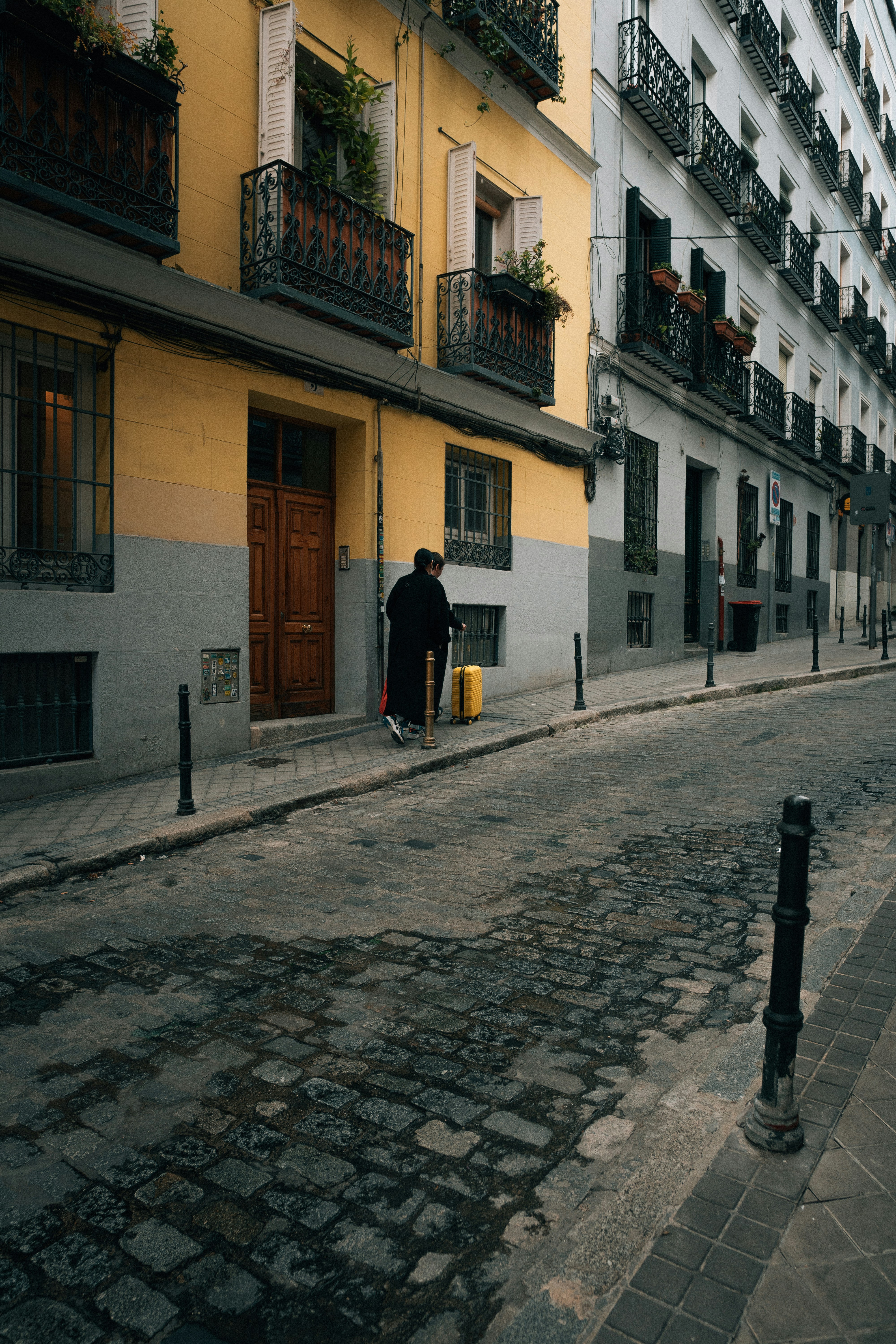 Traveler with a Yellow Suitcase on a Cobblestone Street in a European Alley