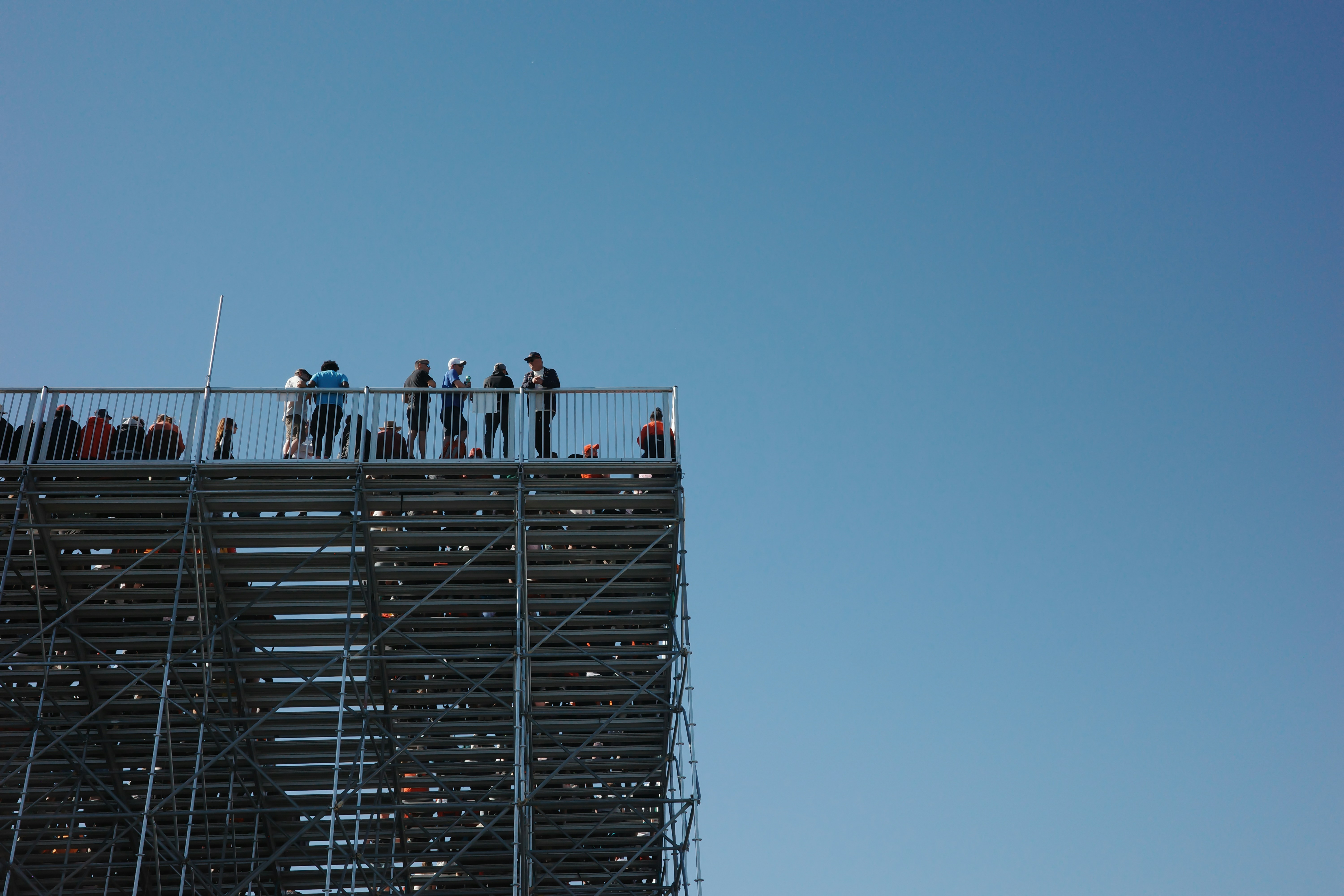 People on a steel viewing platform against a clear blue sky
