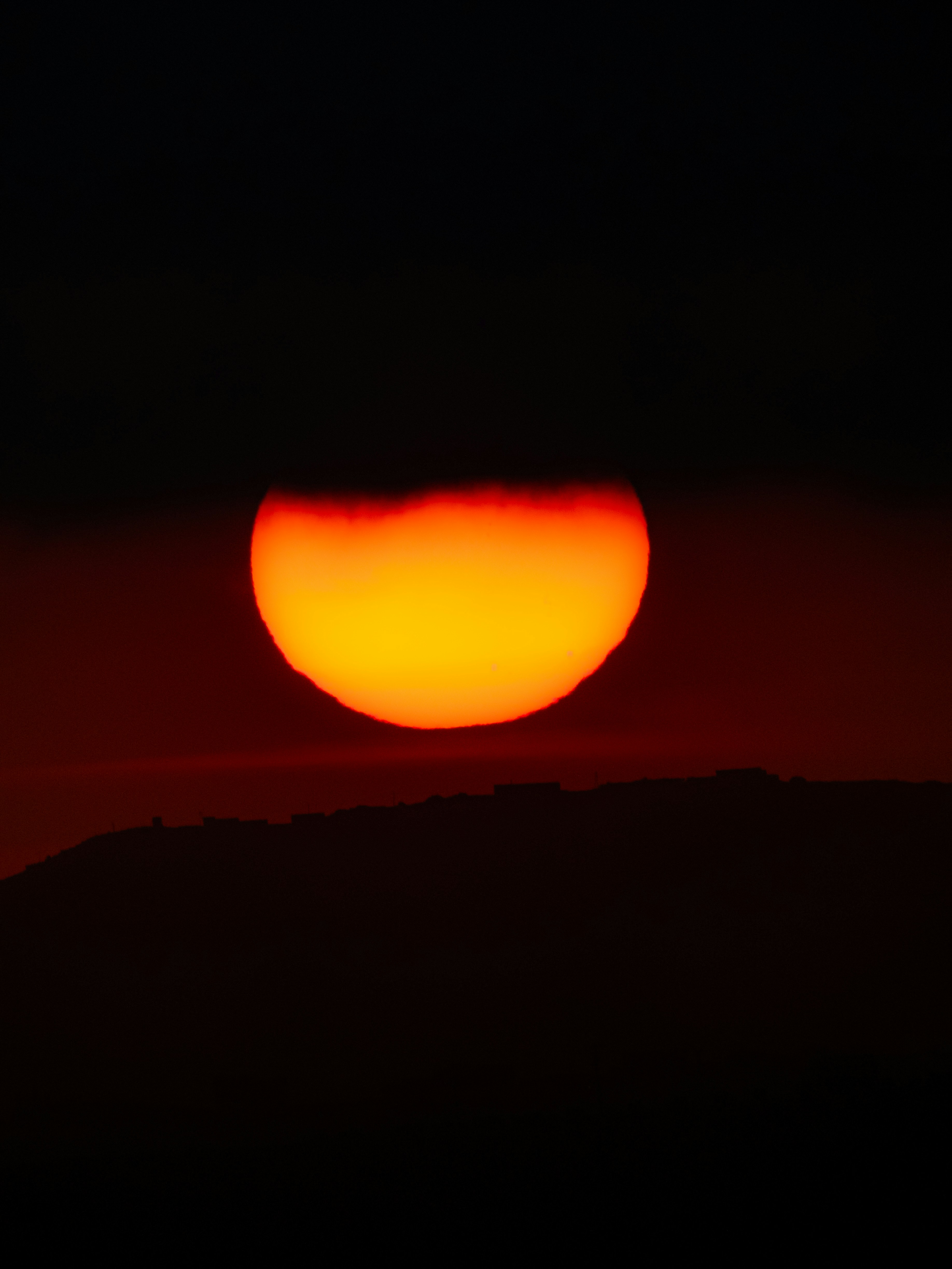 A vibrant orange sun setting behind dark mountains.