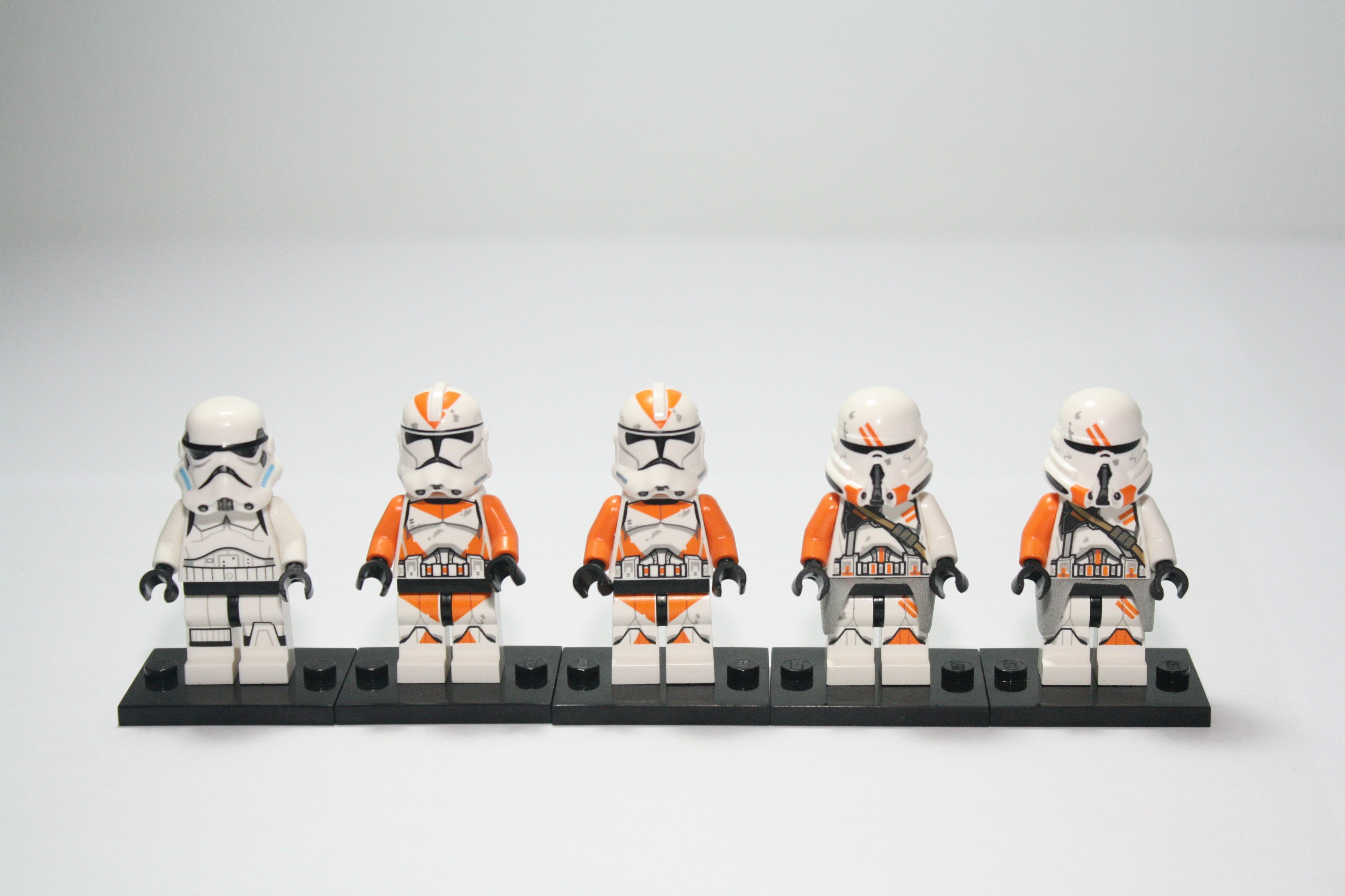 Five LEGO Star Wars clone trooper minifigures, including 212th Attack Battalion clones, standing in a row on black plates against a white background