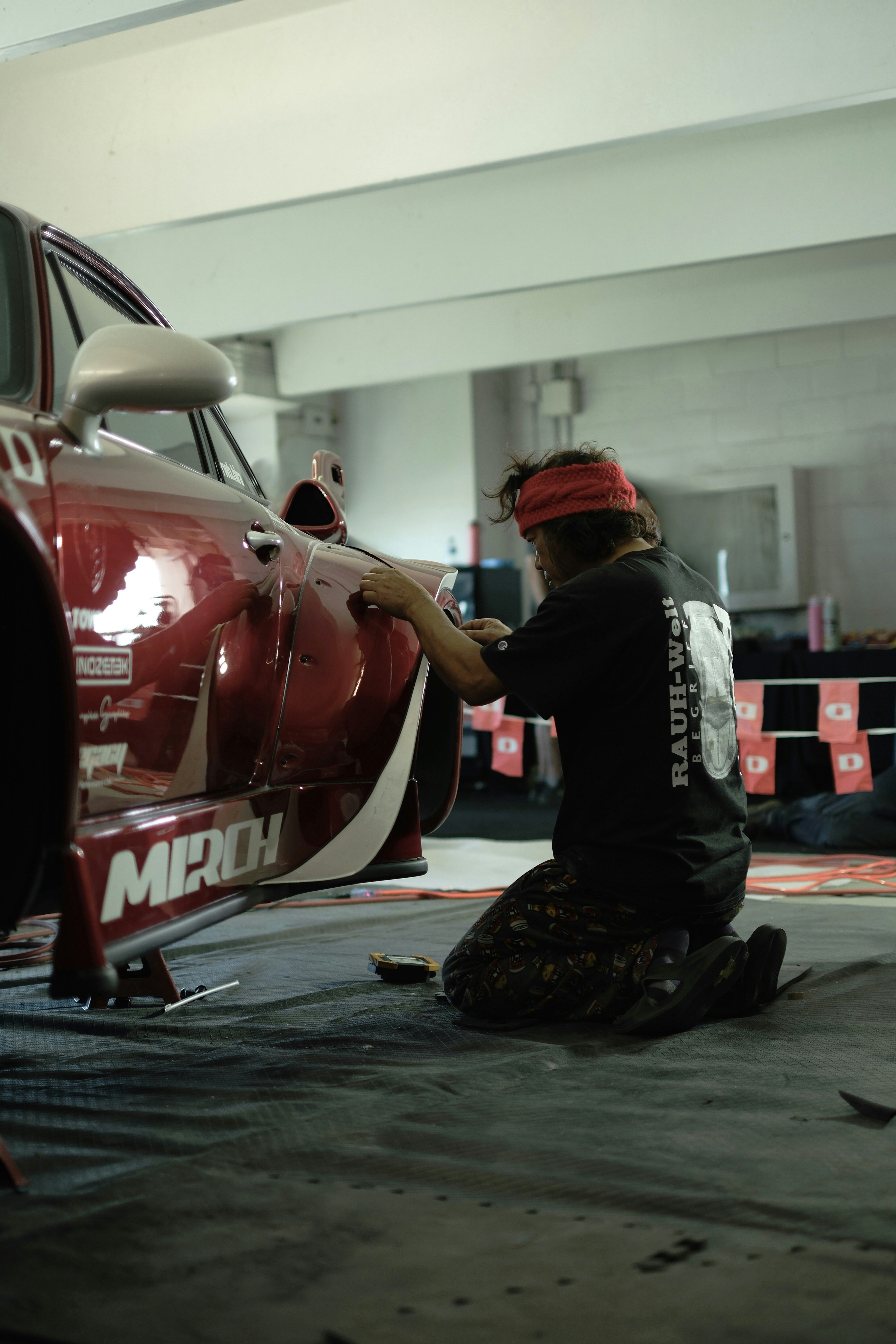 Hands at Work: A Mechanic in Red Bandana Tends the Red Racing Car