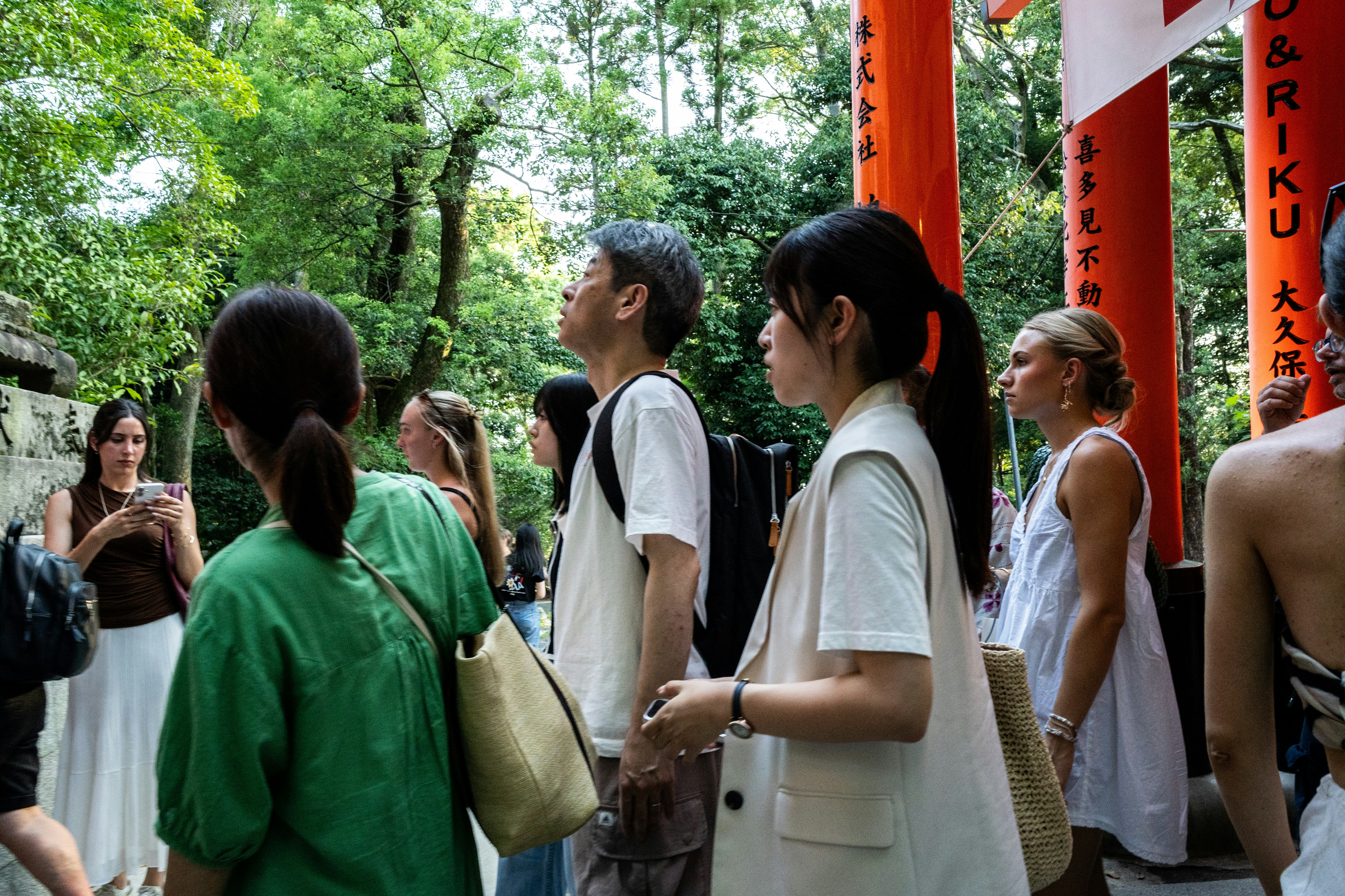 People walking near red torii gates and green trees.