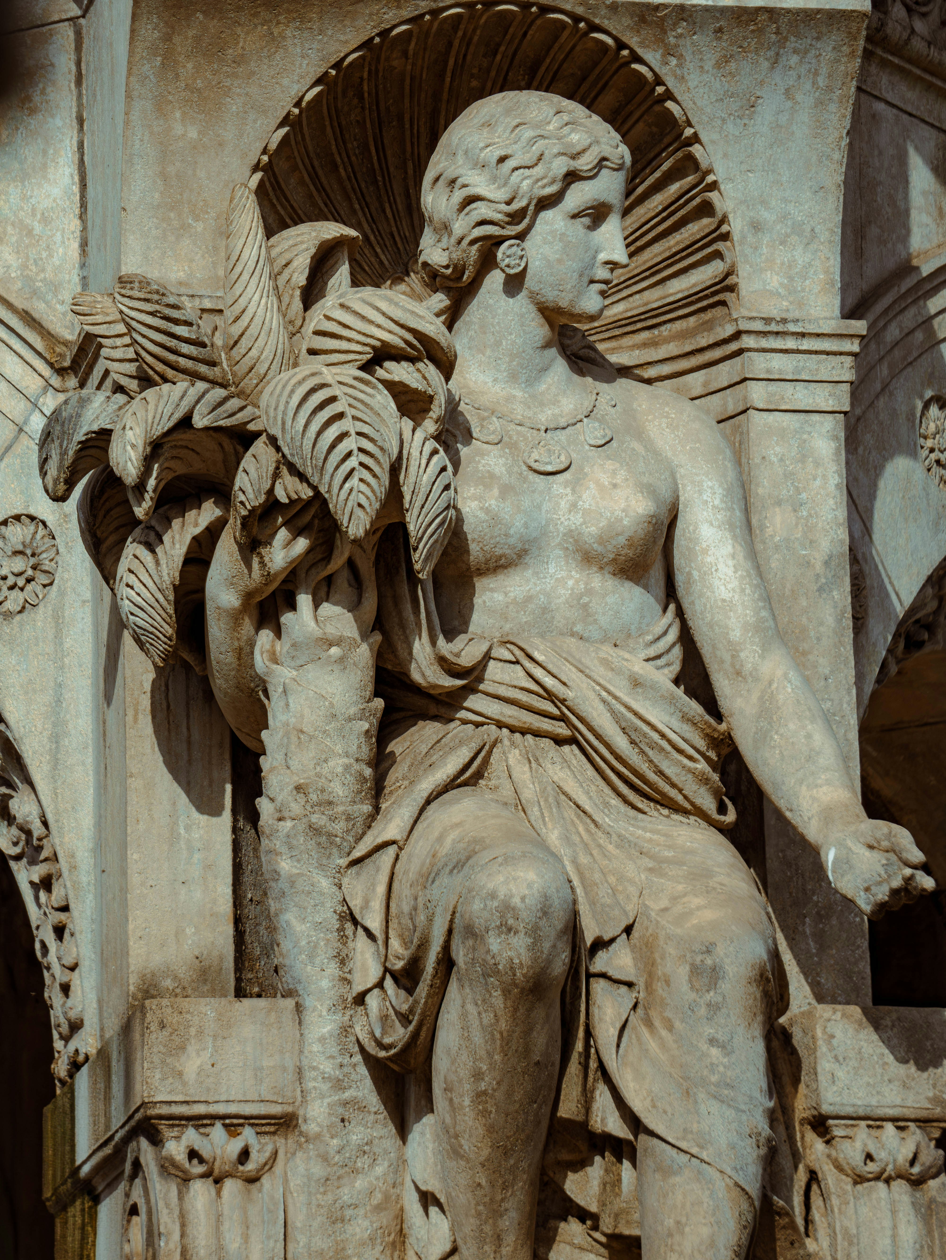 Classical stone statue of a woman holding a palm frond.