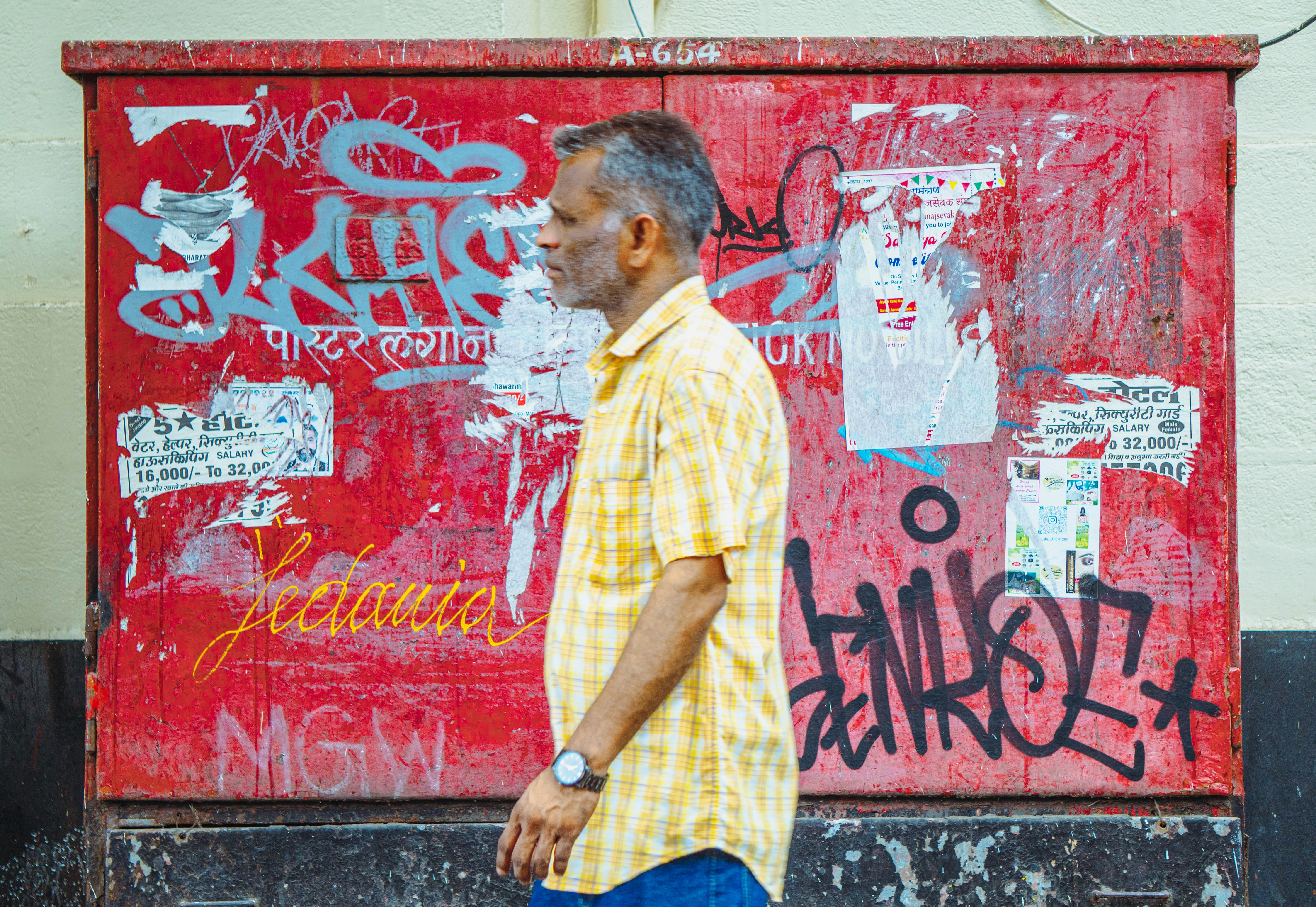 Man walks past a red wall with graffiti.