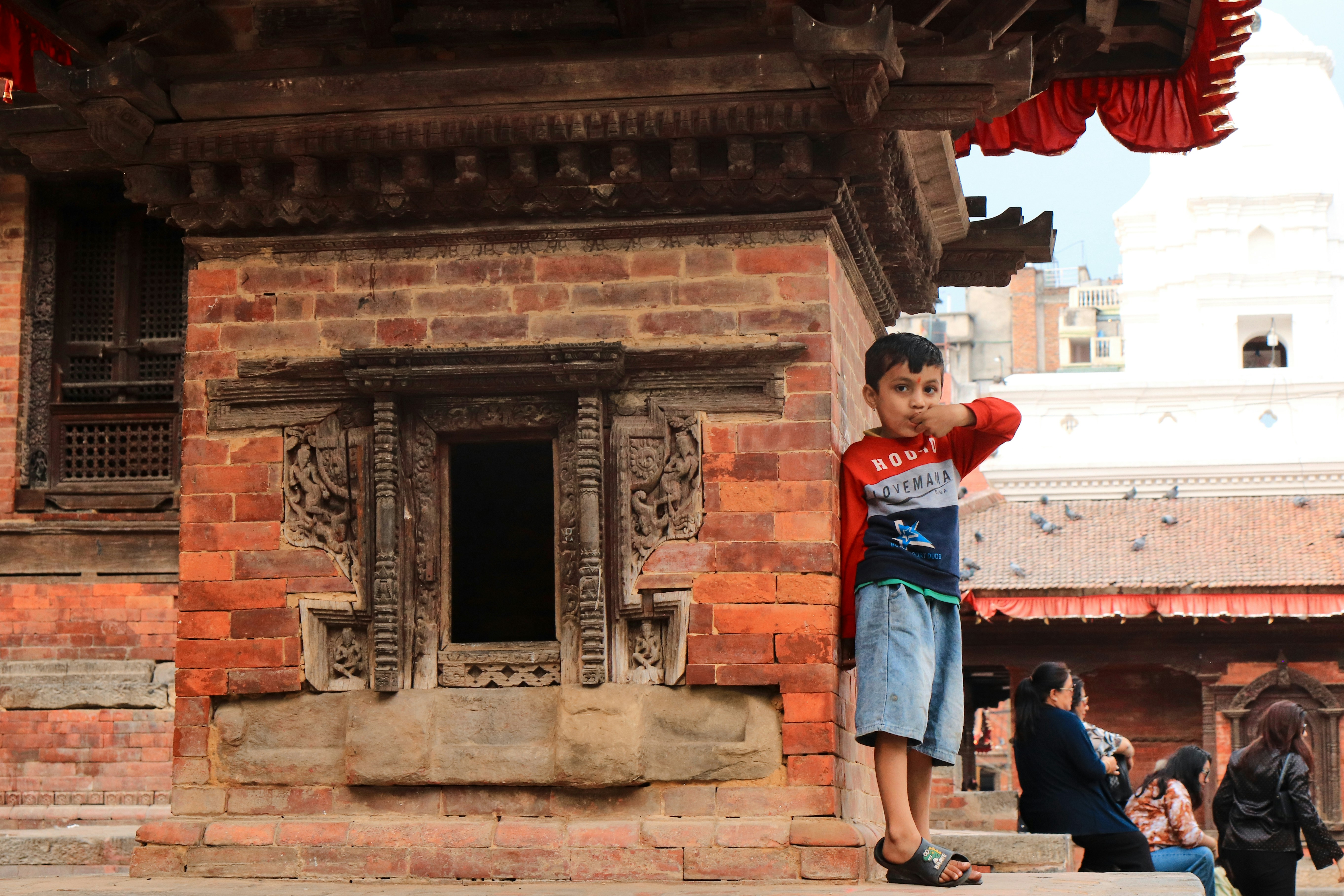 Boy on a brick ledge beside a carved temple facade