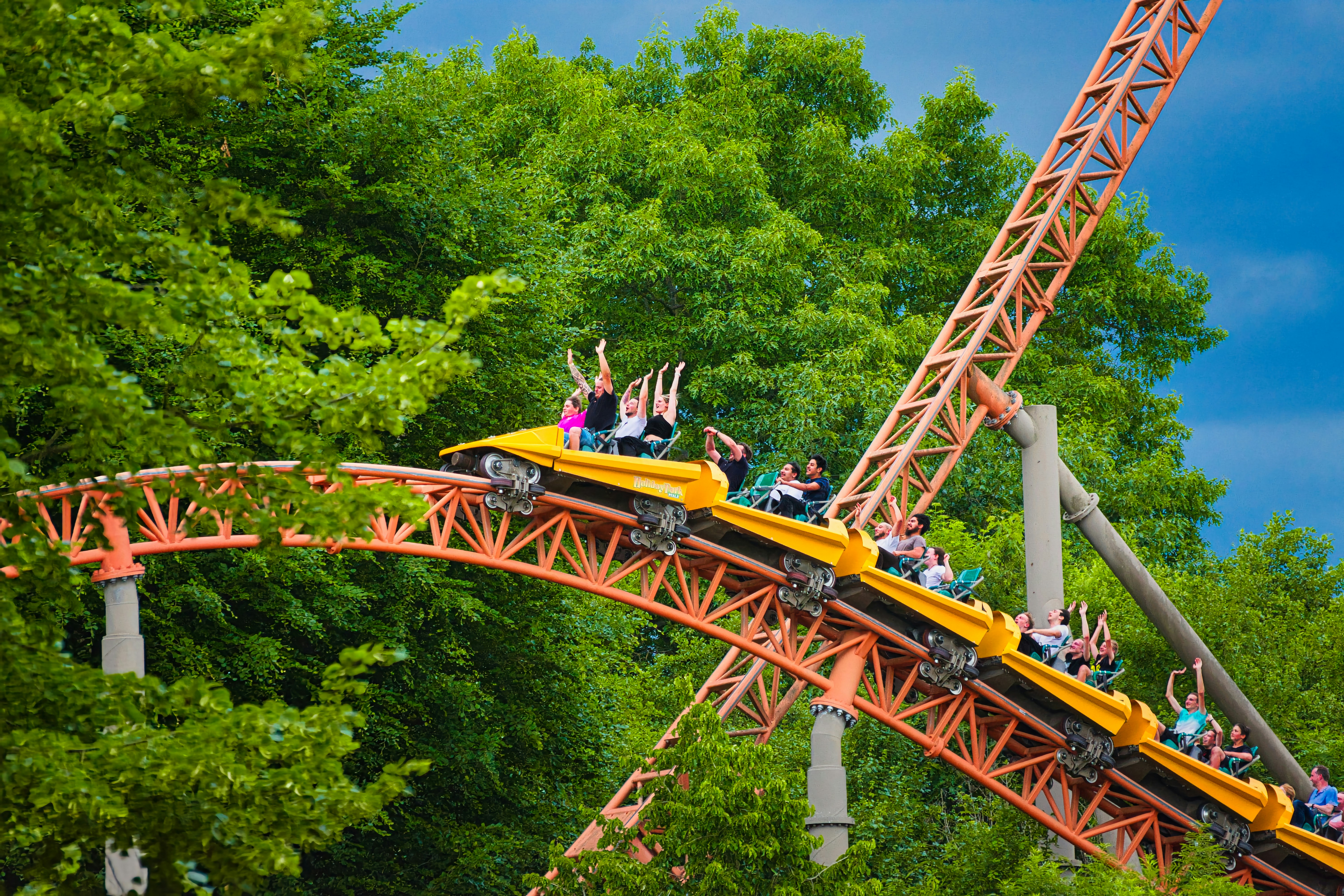Yellow Roller Coaster Car Cresting a Bright Orange Track Amid Lush Greenery