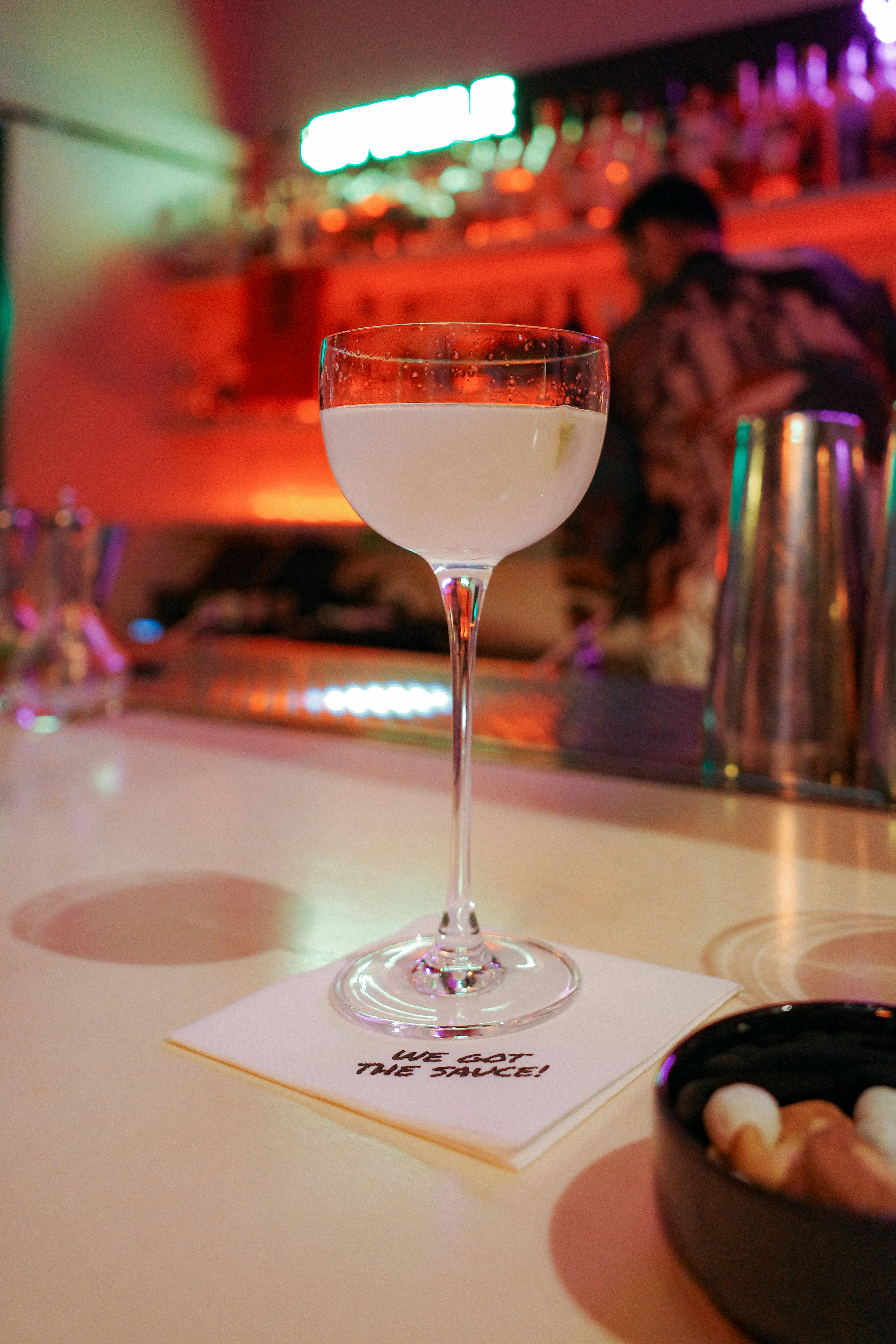 Stemmed Glass in Neon Night: A Bar Scene with a Pale Cocktail