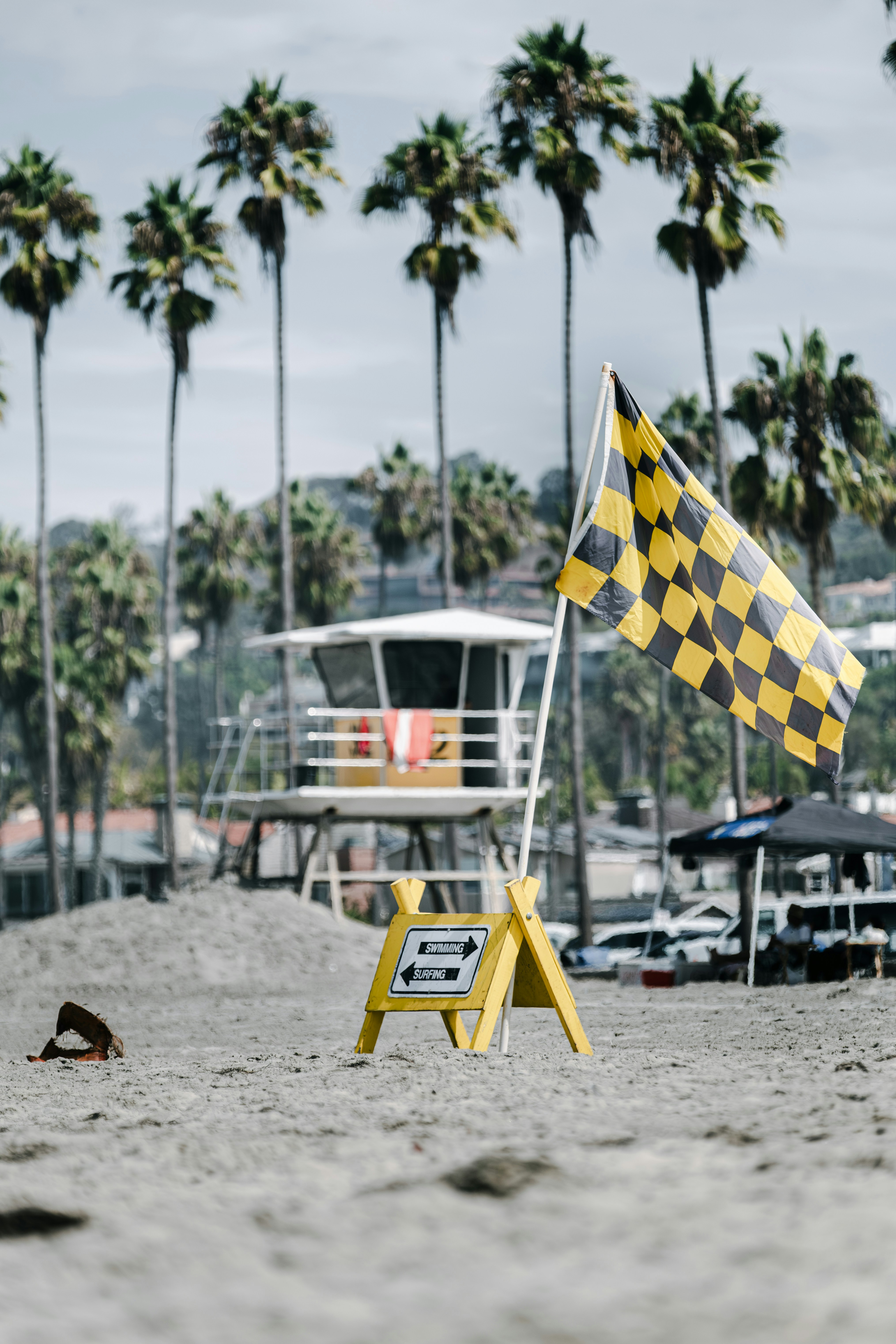 Yellow checkered flag, lifeguard tower, and palm trees on beach.