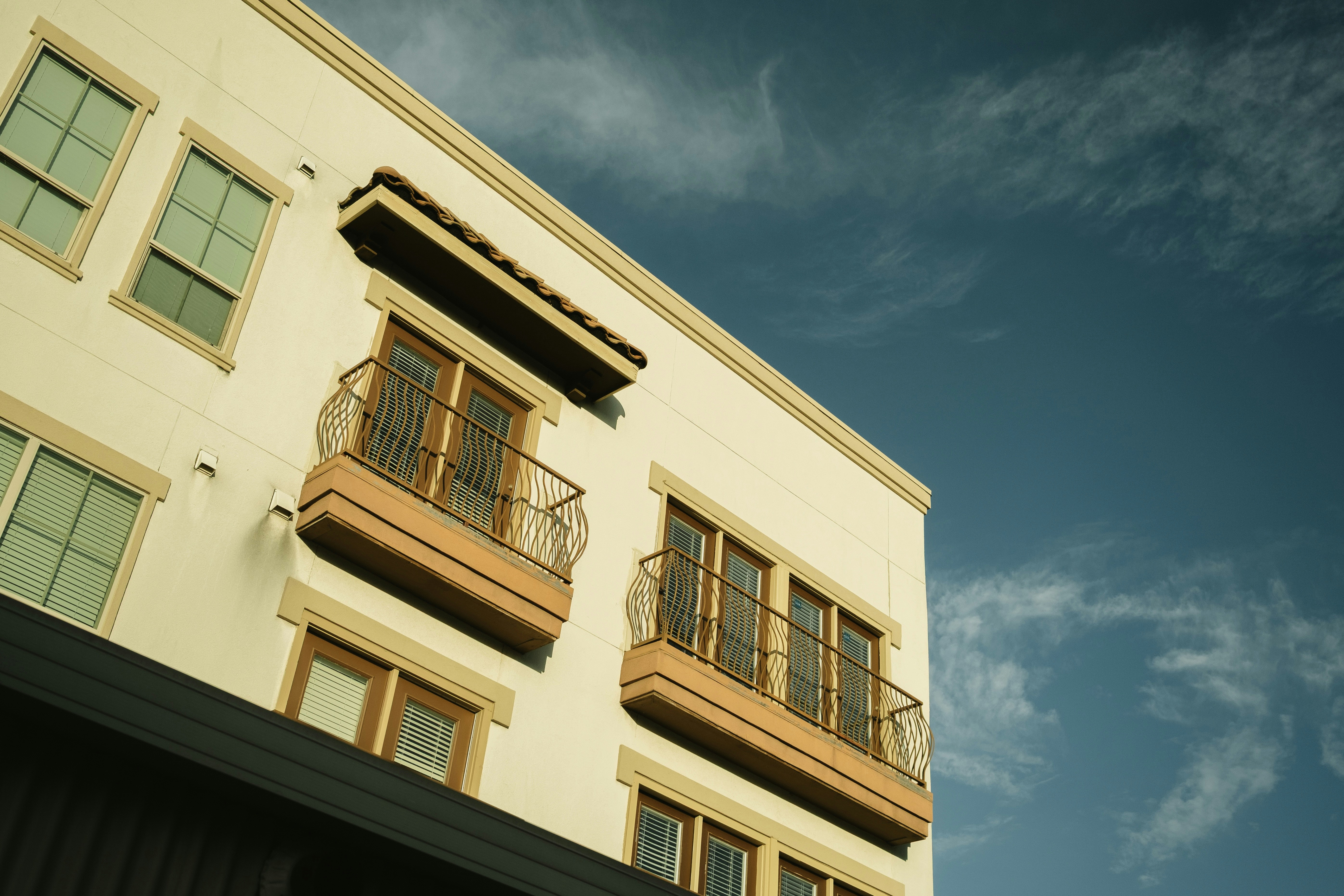 Cream-colored building with balconies under a cloudy blue sky.