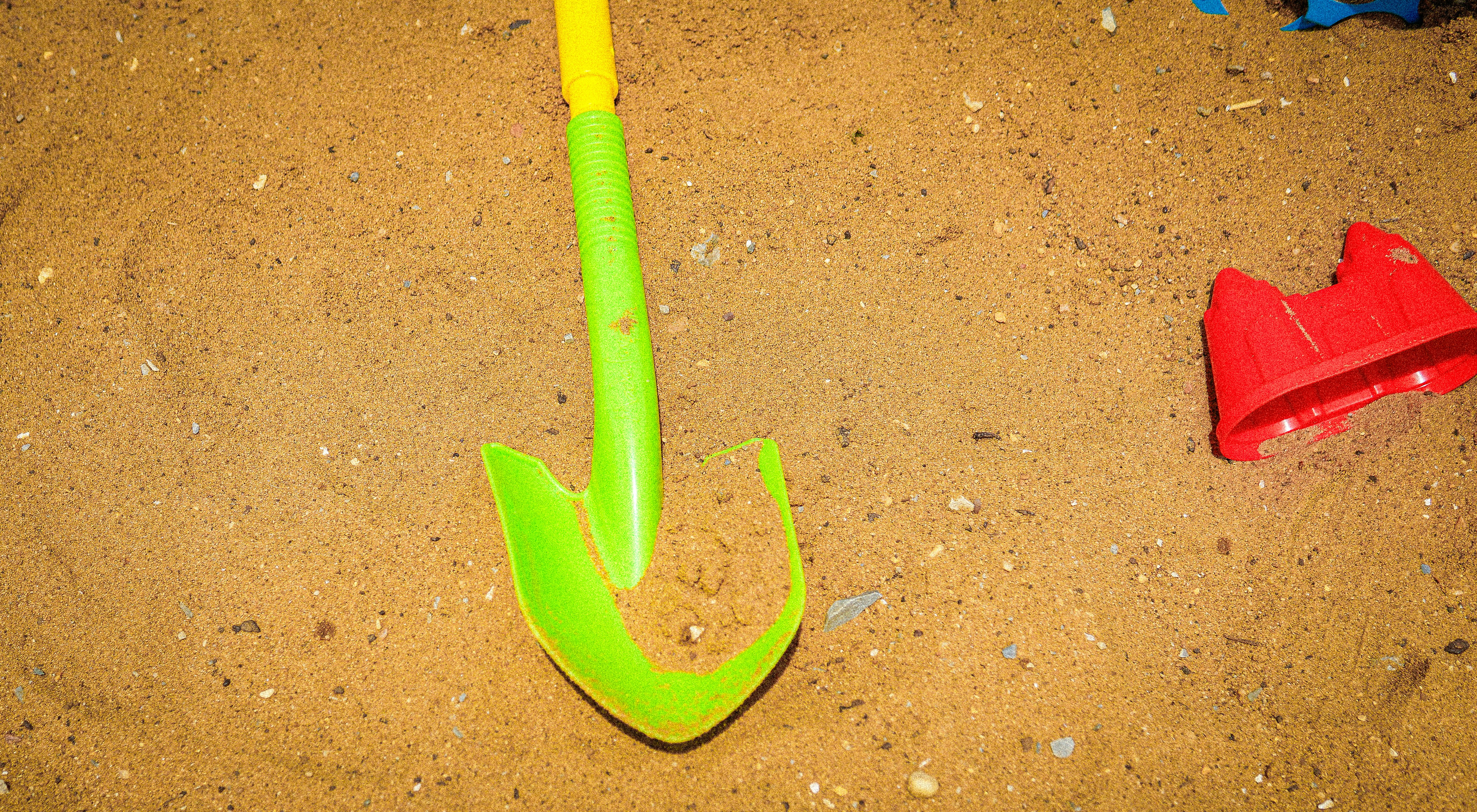 Bright Green Shovel Blade in sandy soil with Red Cap Fragments