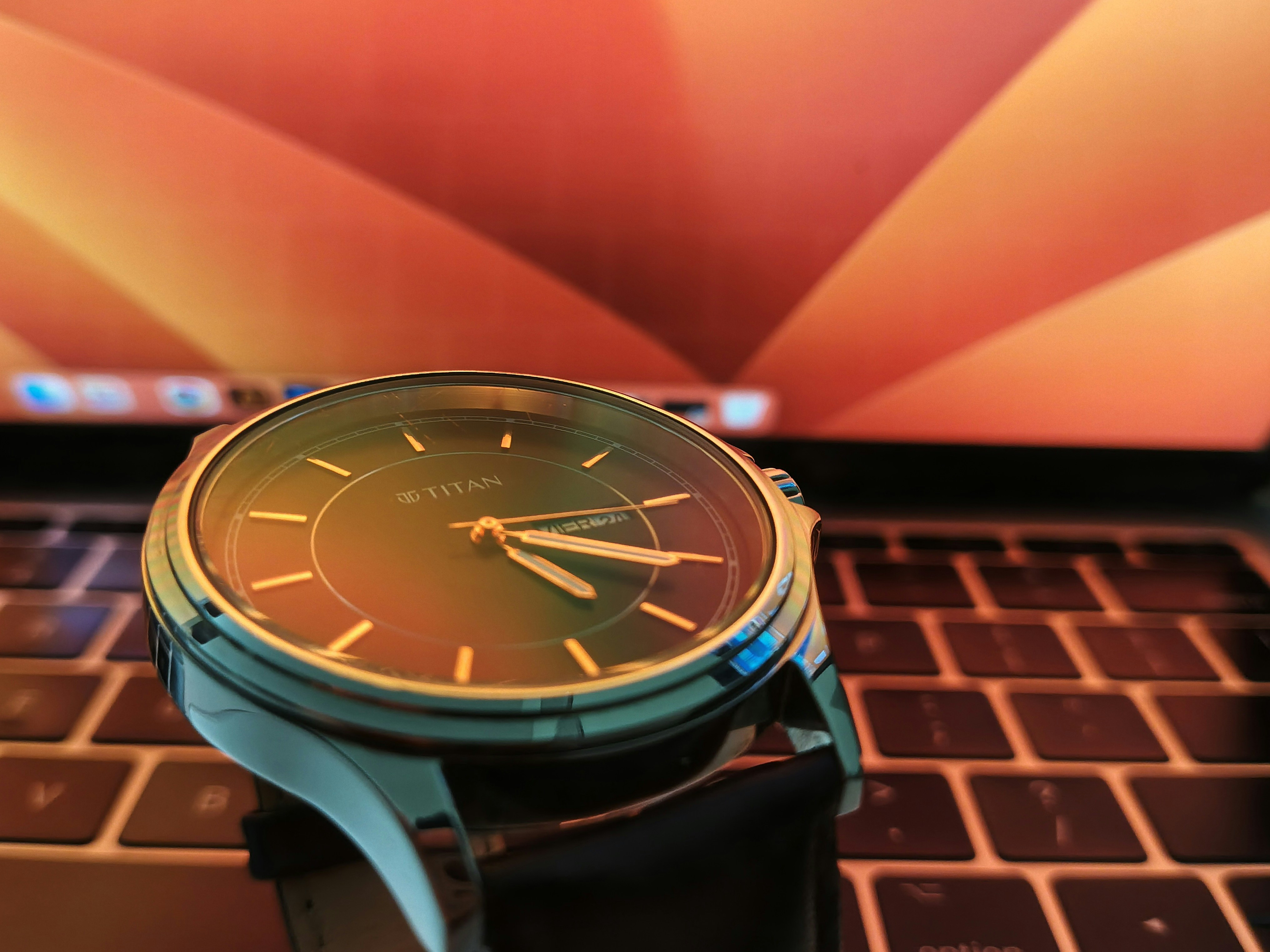 Close-up of a minimalist Titan wrist watch resting on a MacBook keyboard under warm evening light.