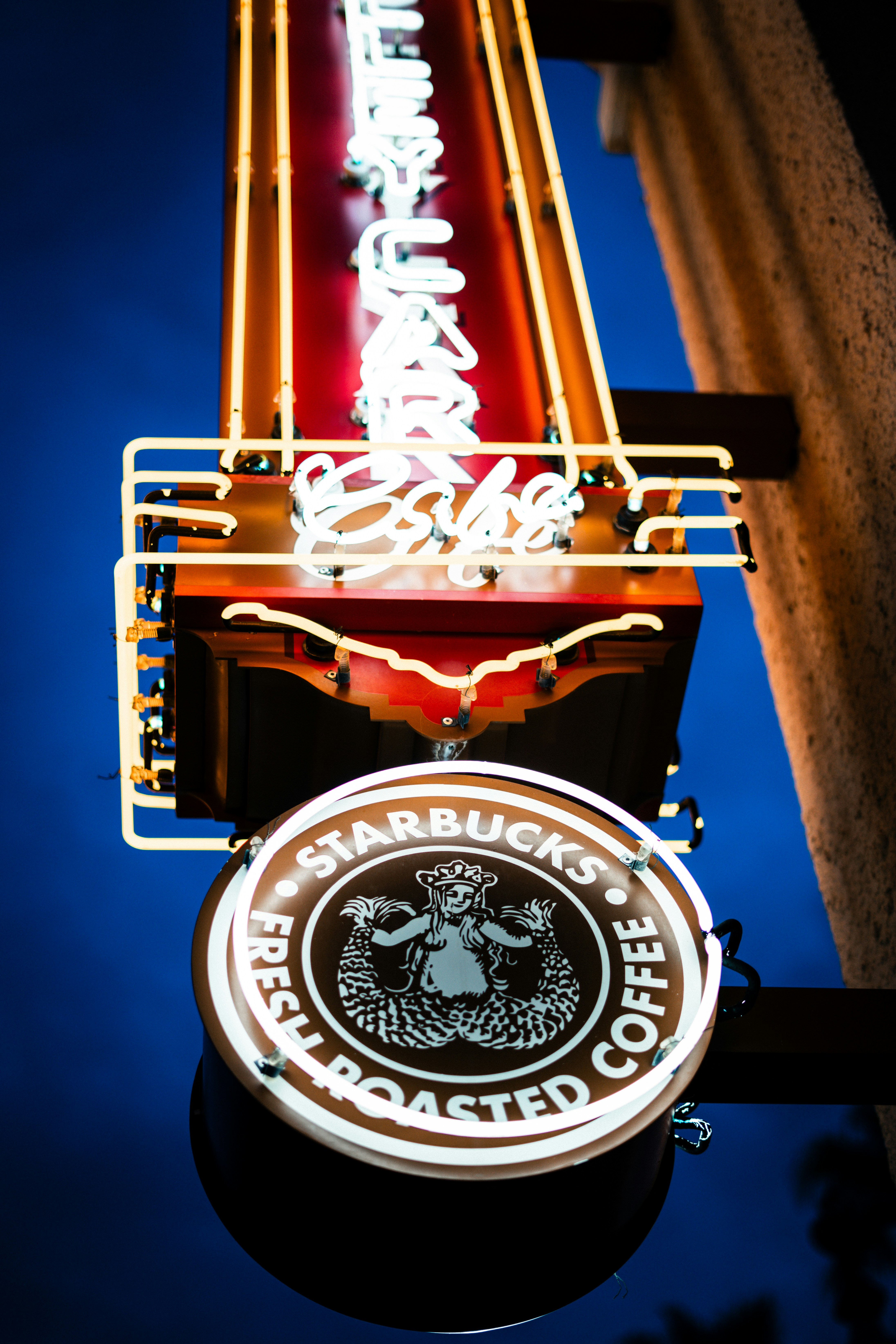 Neon Starbucks Sign Pierced by Night: A Glowing Circular Emblem Under Vertical Neon Trails